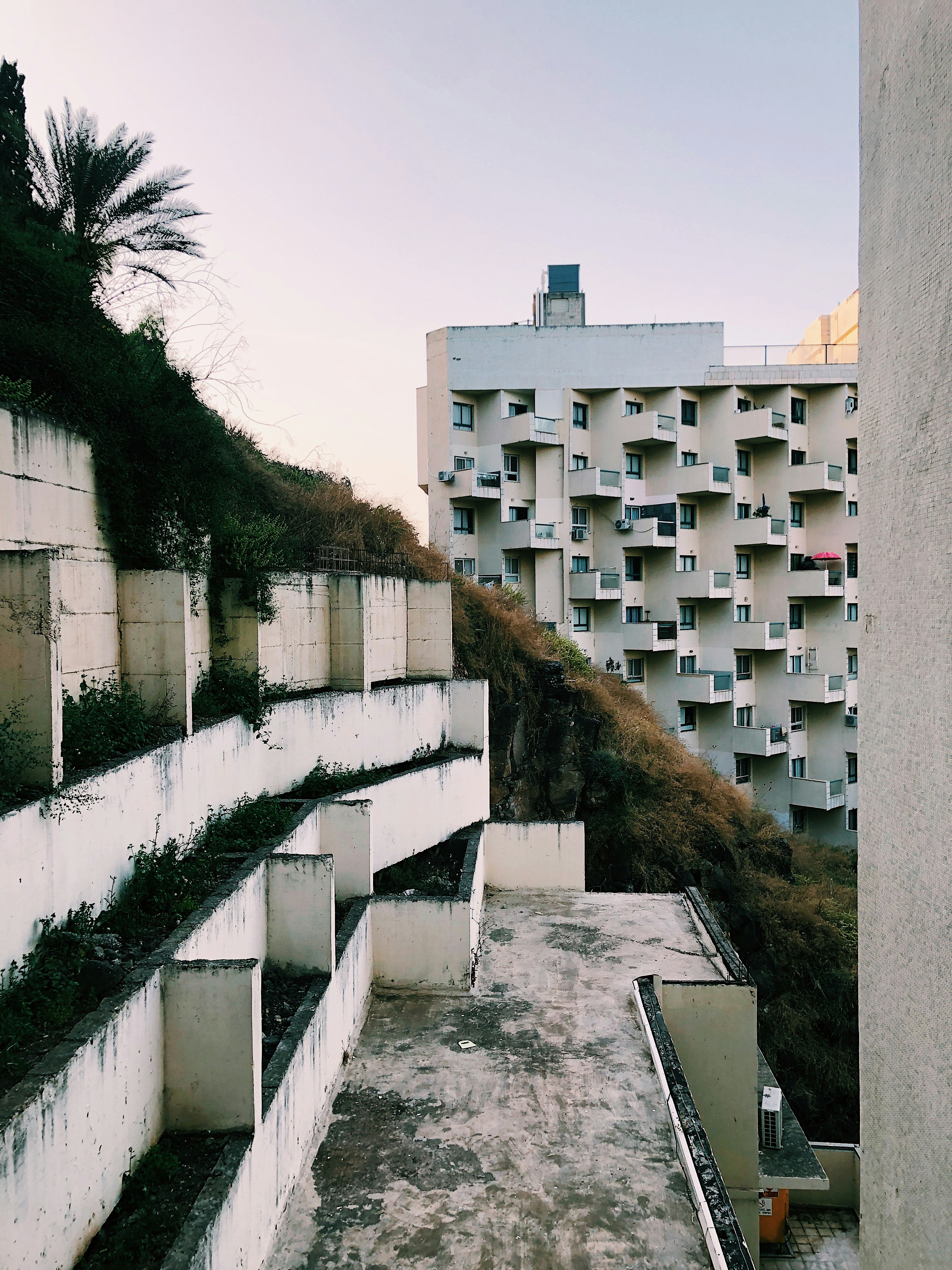 Layered concrete terraces with greenery juxtaposed against a modern building facade featuring unique window patterns.