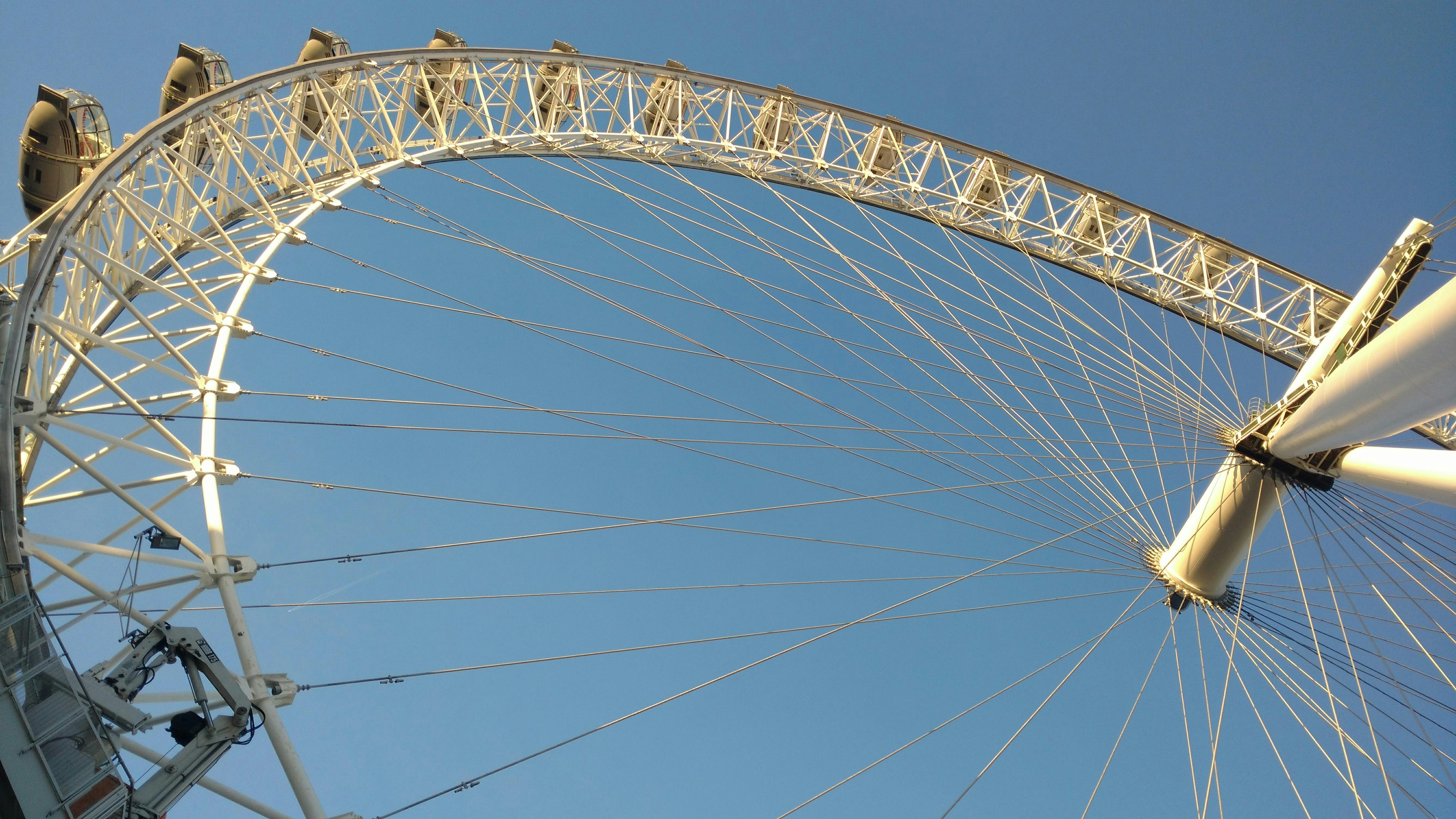 A Ferris wheel's intricate structure against a clear blue sky, showcasing its engineering elegance and the tension of its supporting cables.