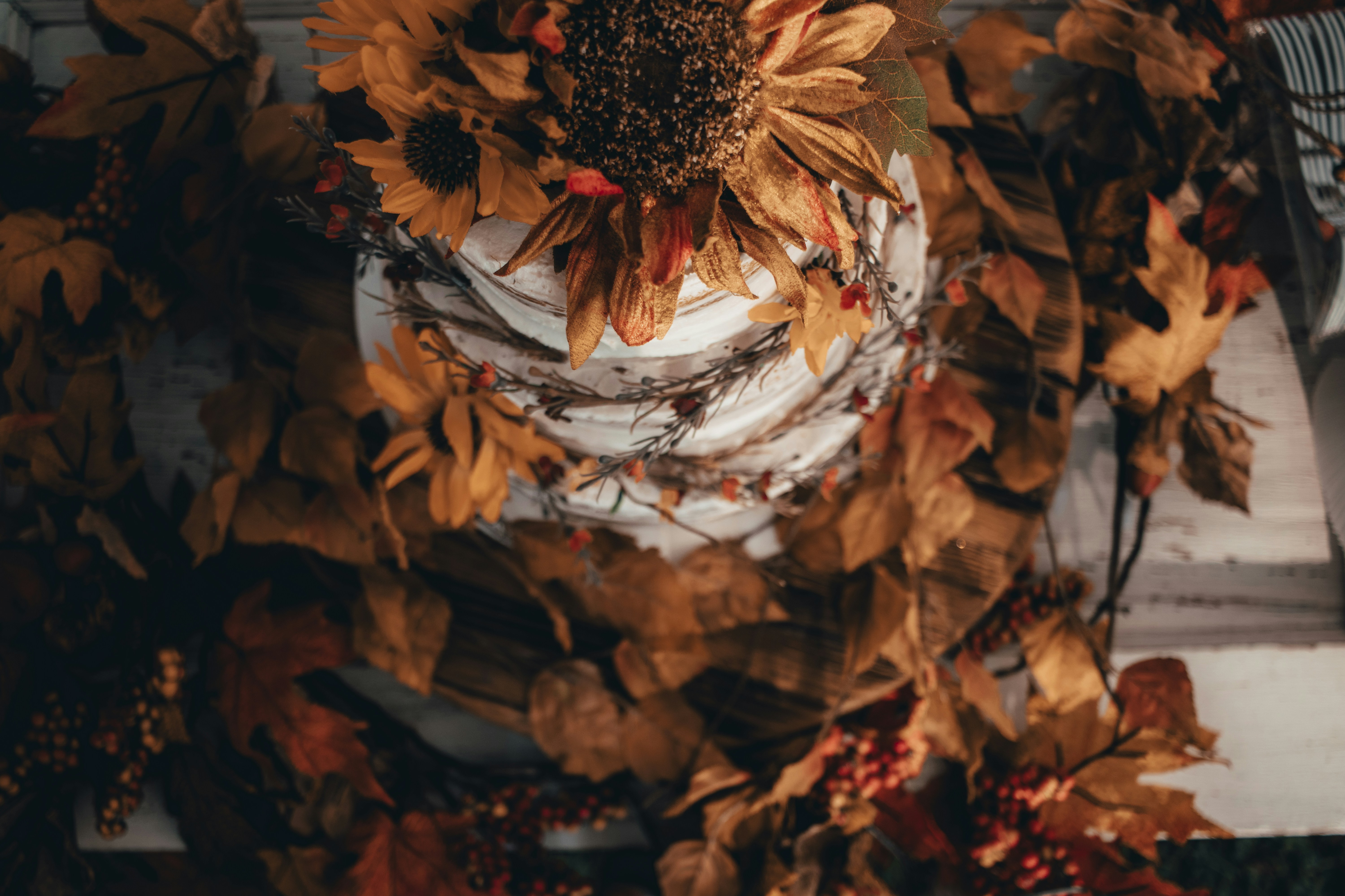 Three-tiered cake decorated with sunflowers and autumn leaves, surrounded by a rustic arrangement of foliage and berries.