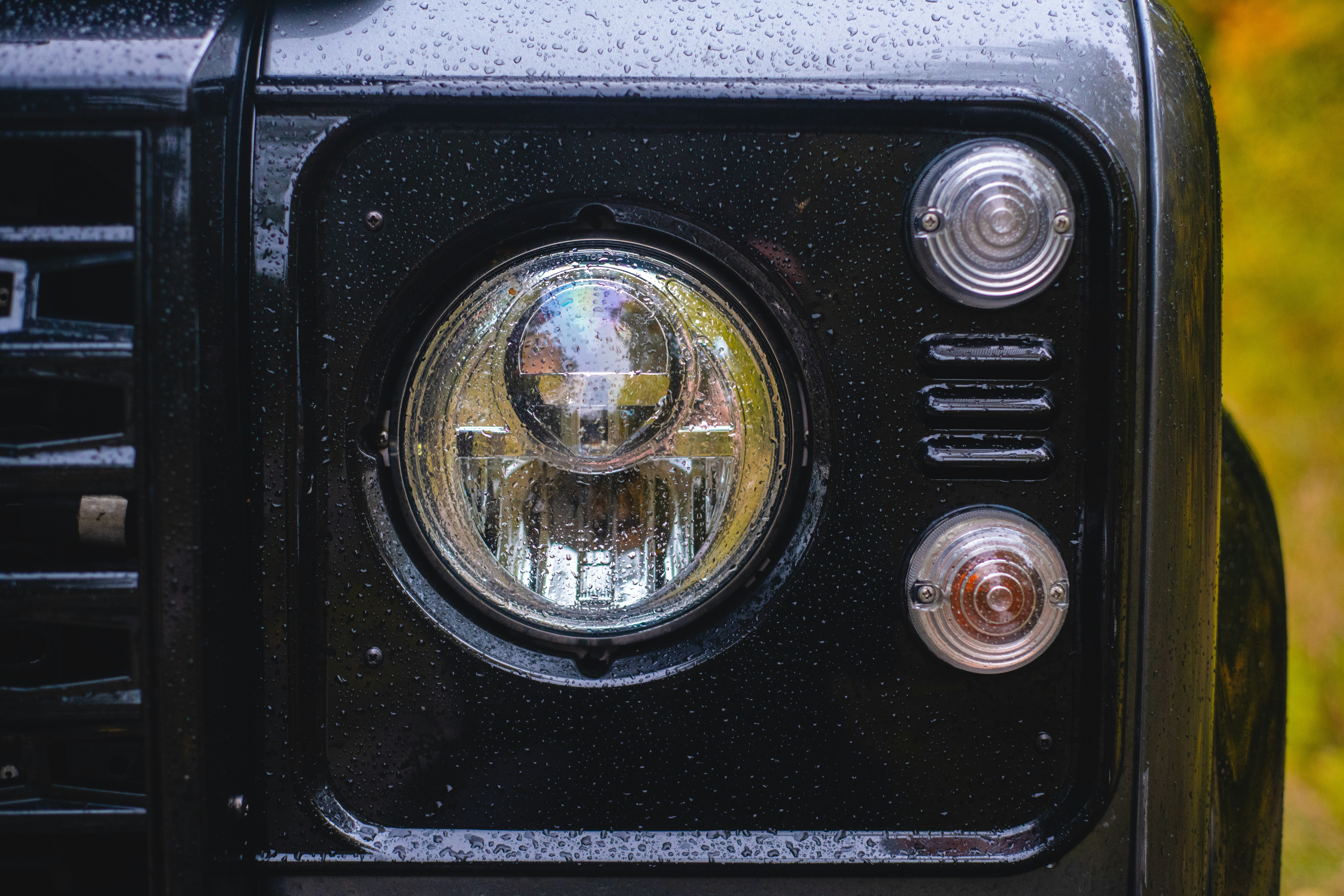 Close-up of a vehicle's headlight and turn signals, showcasing intricate details and water droplets on the surface.