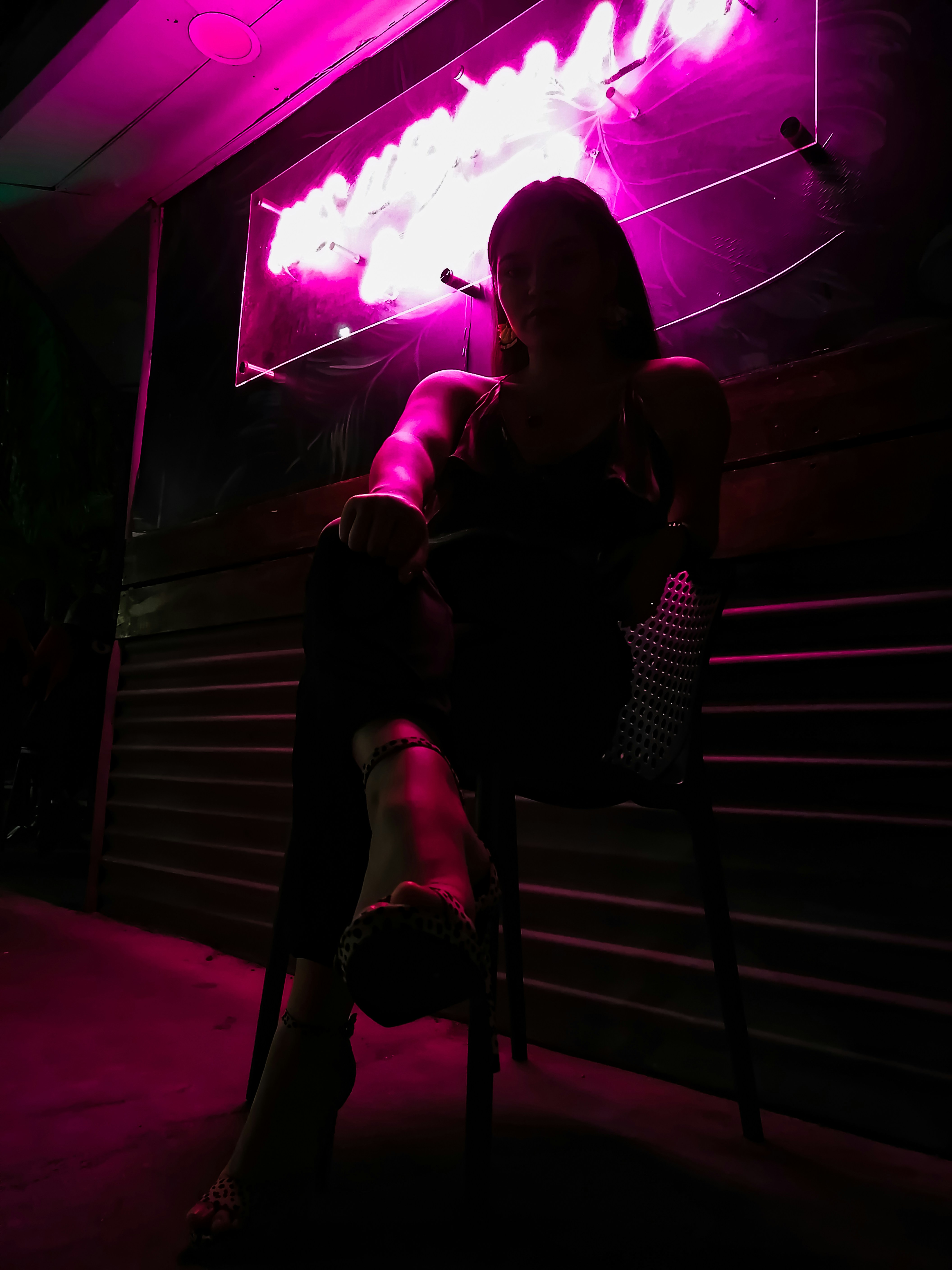 Silhouette of a person seated under vibrant pink neon signage at night.