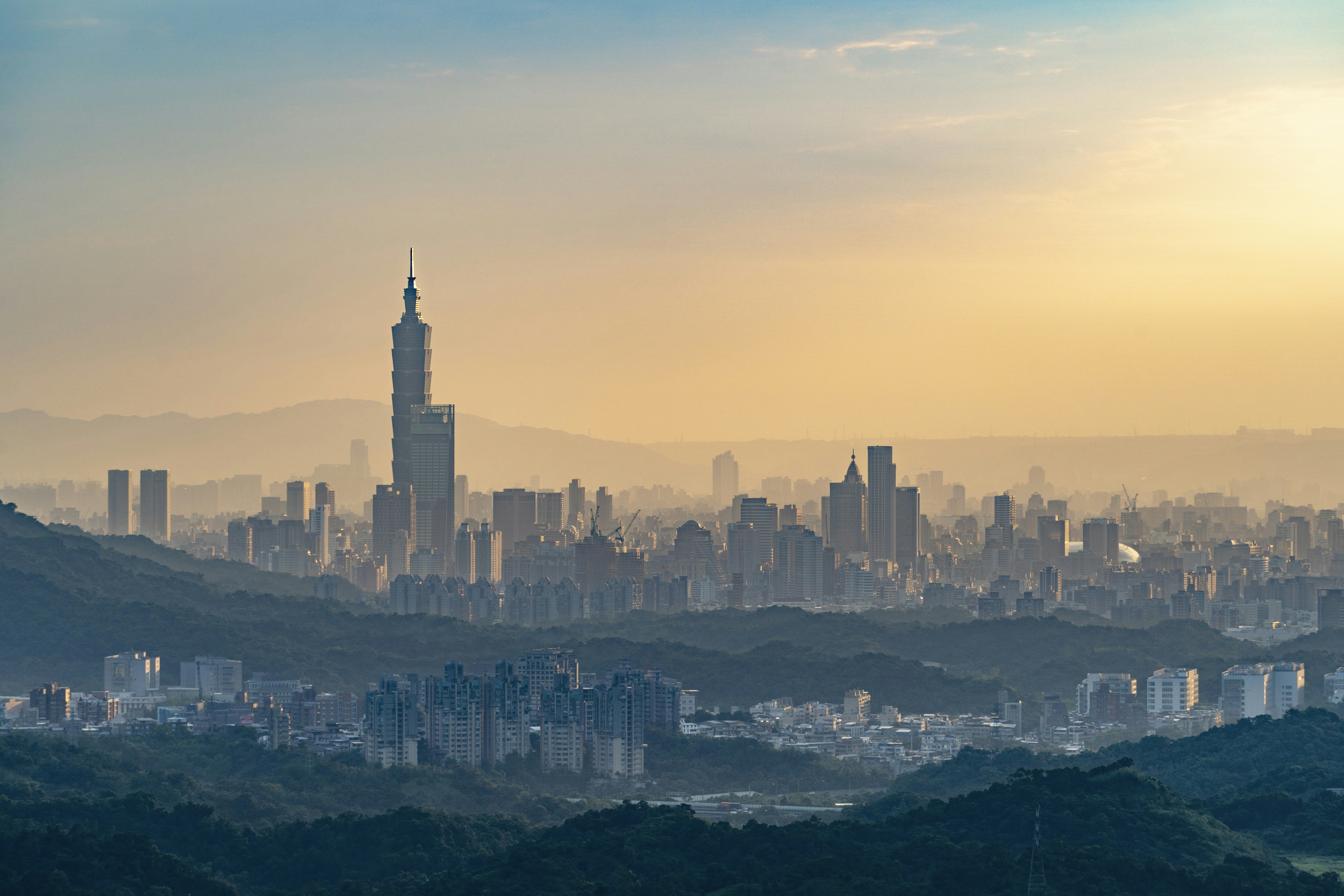 Skyline of a sprawling city under a hazy sunset, featuring a prominent tower amidst the urban landscape.