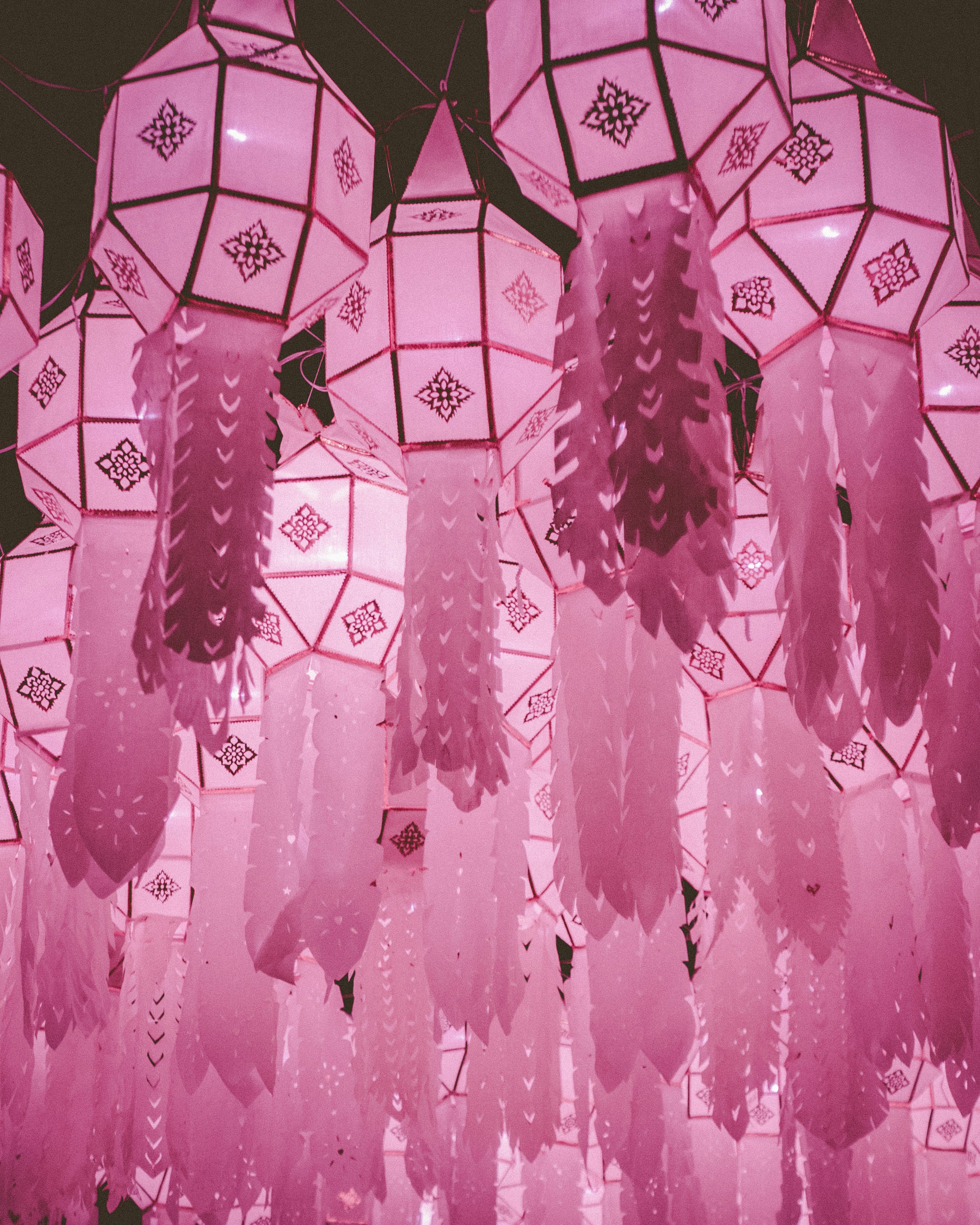 Pink paper lanterns with tassels hang in a dark setting, emitting a warm decorative glow.