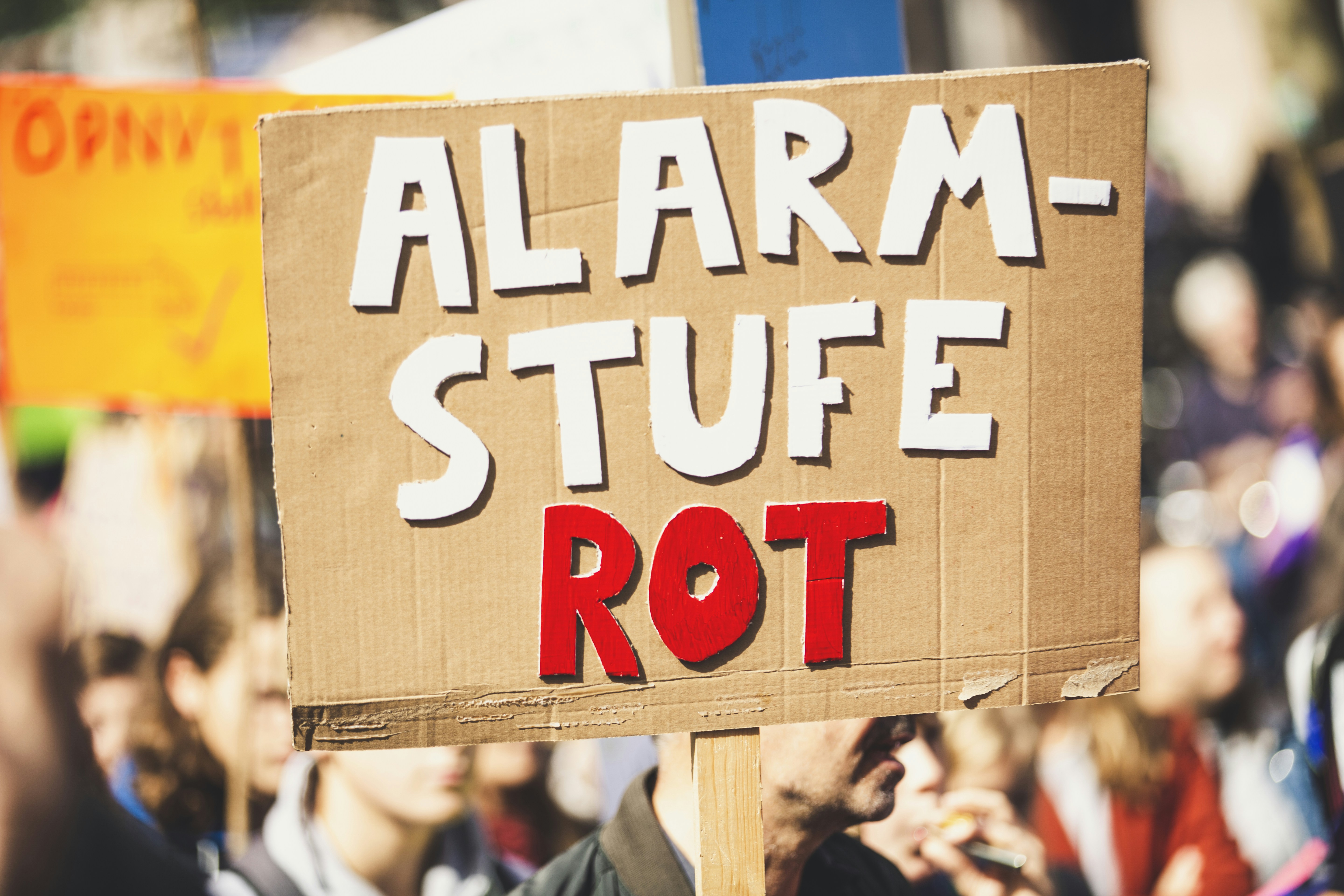 Cardboard sign with bold letters 'ALARMSTUFE ROT' held at a climate protest.