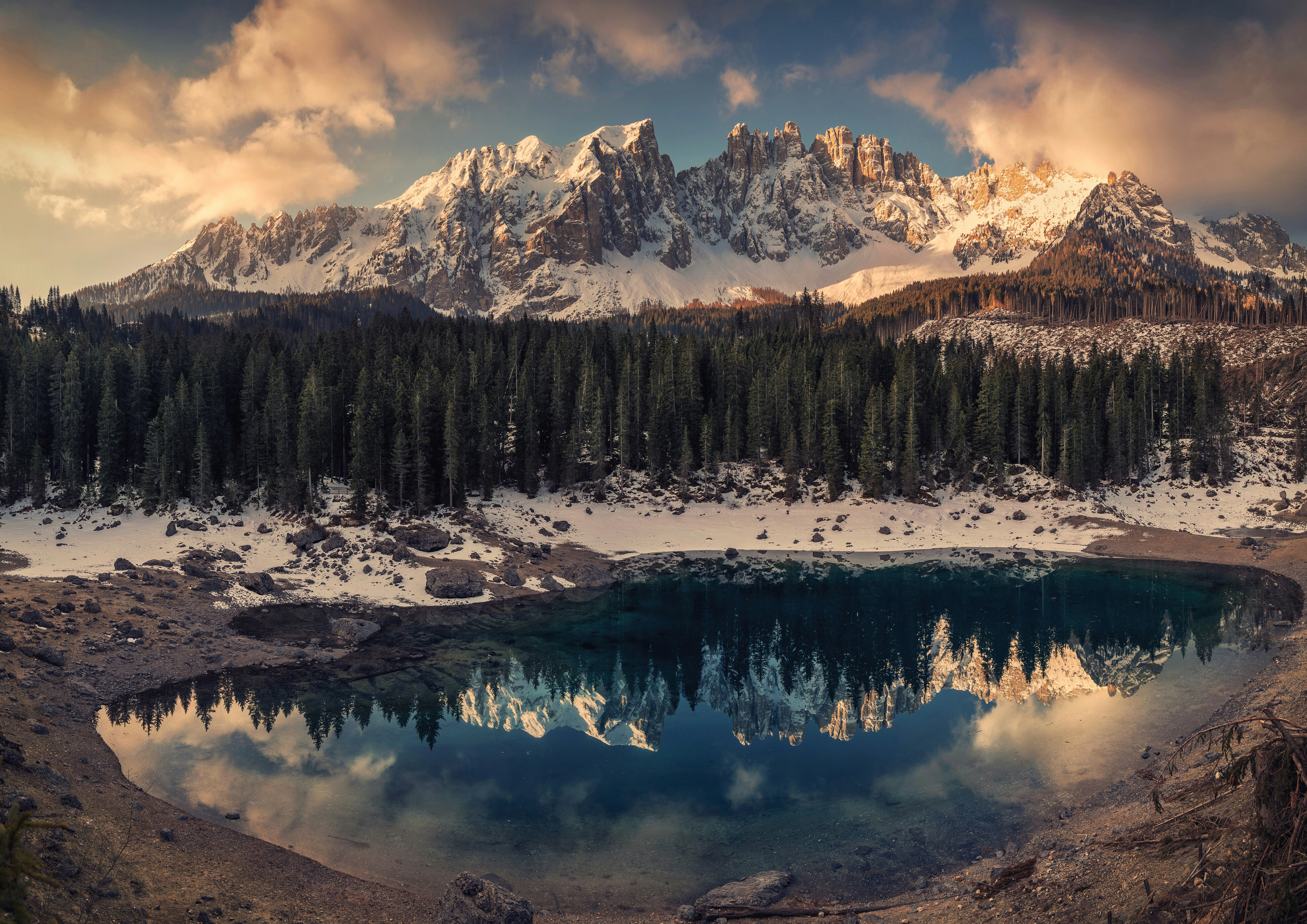 Snow-dusted mountains reflected in the still waters of Karersee under a dramatic sky.