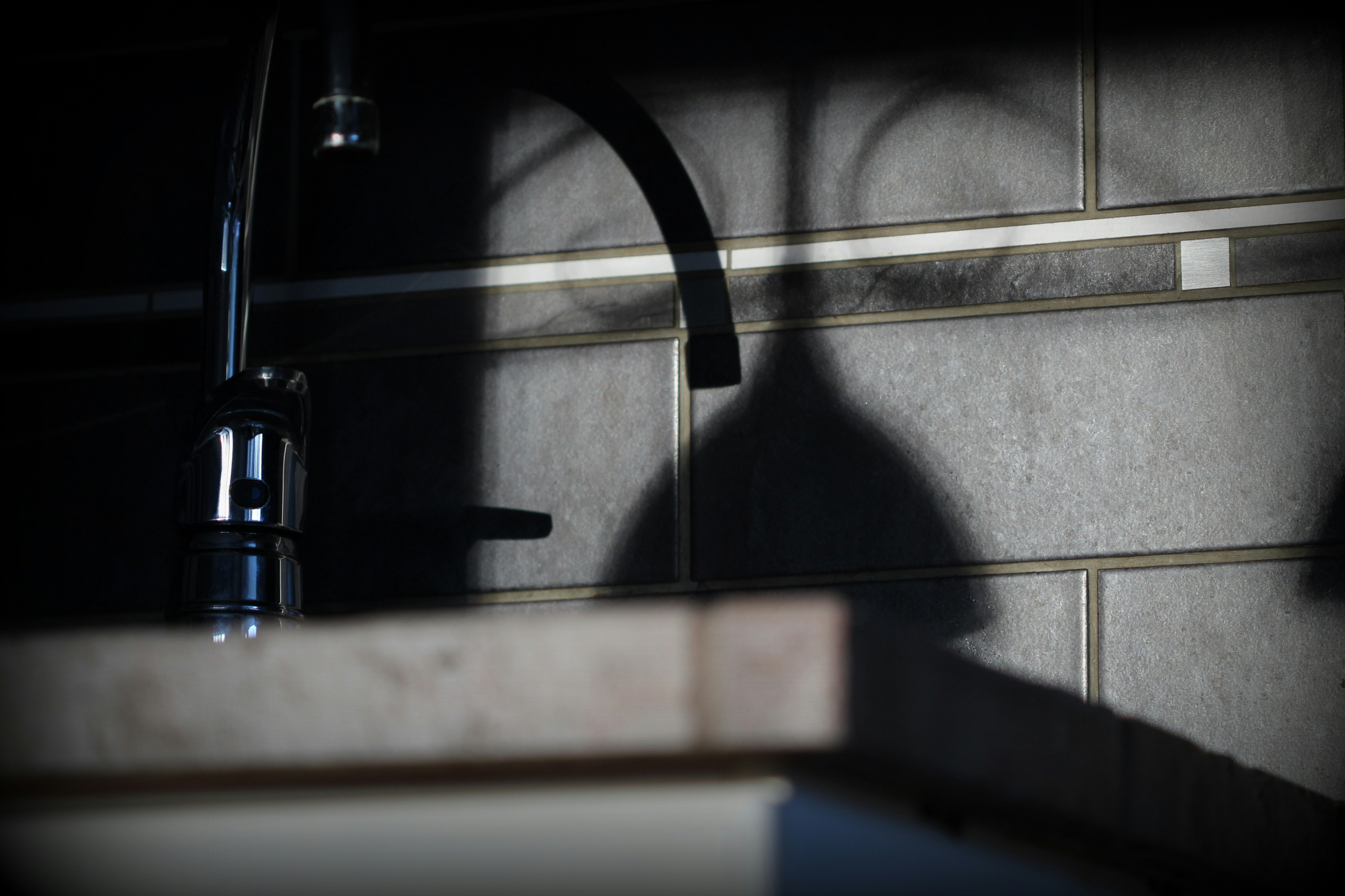Shadowed Figure by the Kitchen Faucet on a Tiled Backdrop