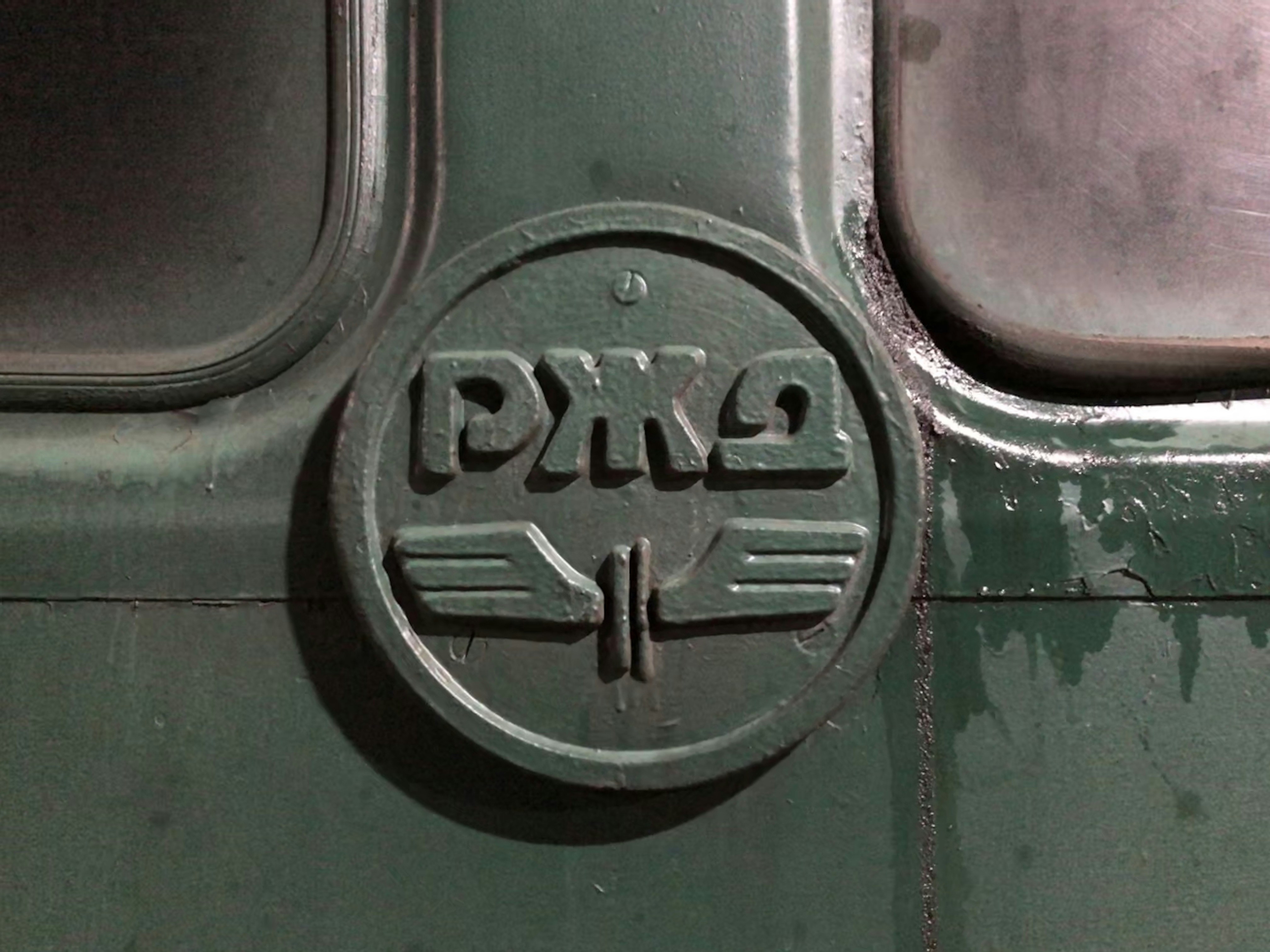 Winged Emblem on Olive-Green Metal: A Close-Up of a Weathered Vehicle Logo