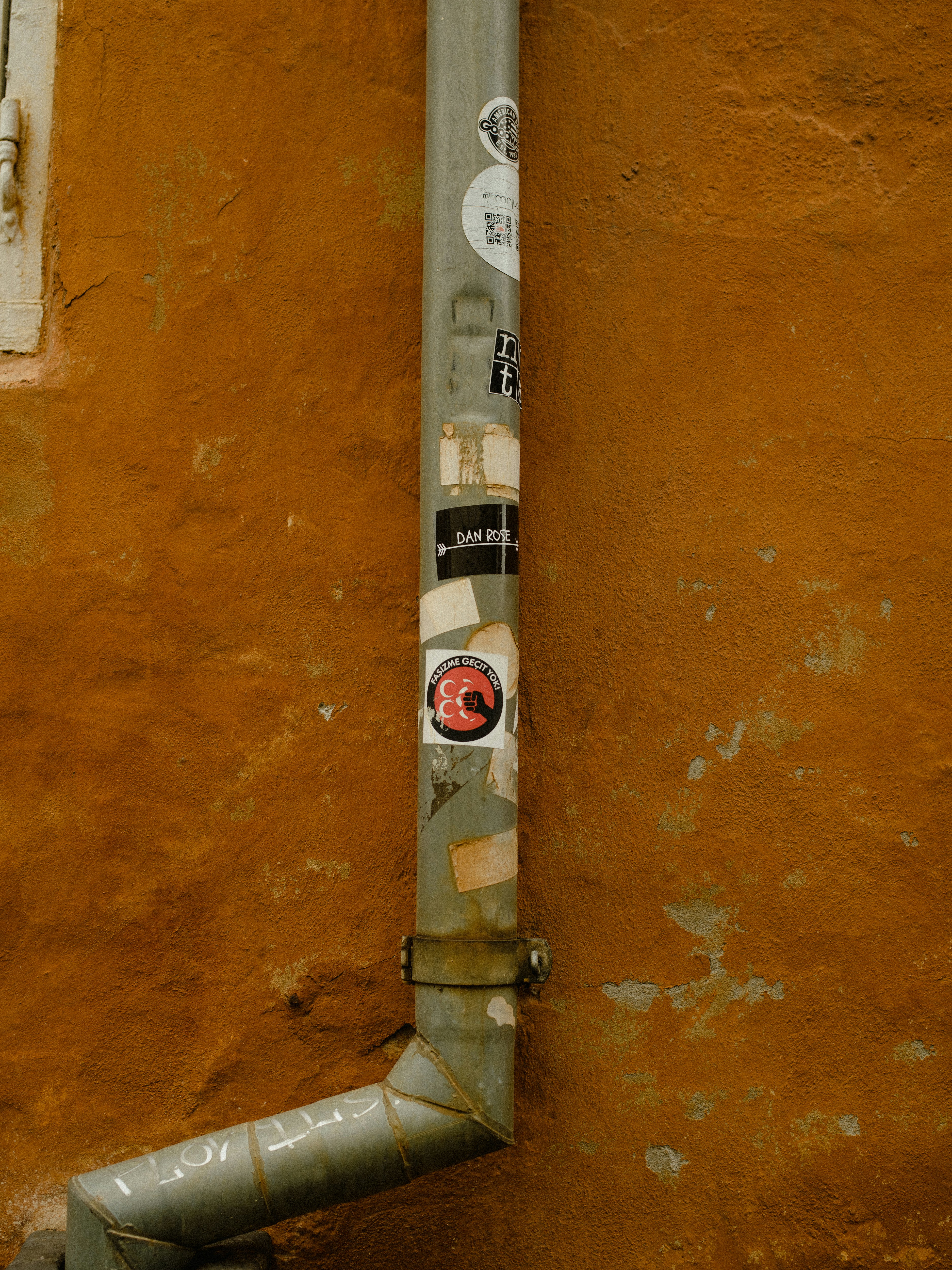 Stickered Pipe Silhouette on a Sun-Warmed Orange Wall