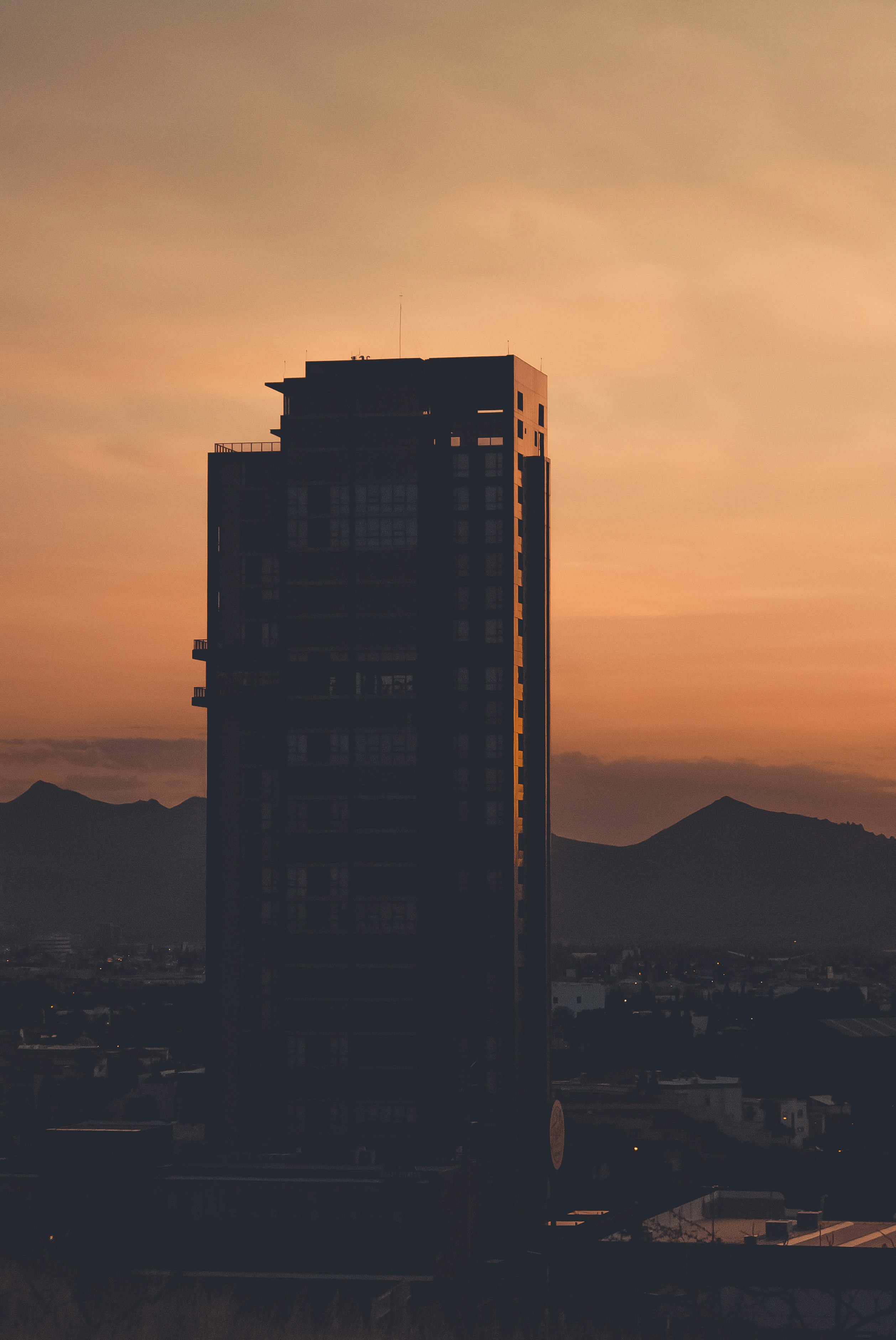 Silhouette of a modern building set against a warm, gradient sky at sunset, highlighting the interplay of architecture and nature.