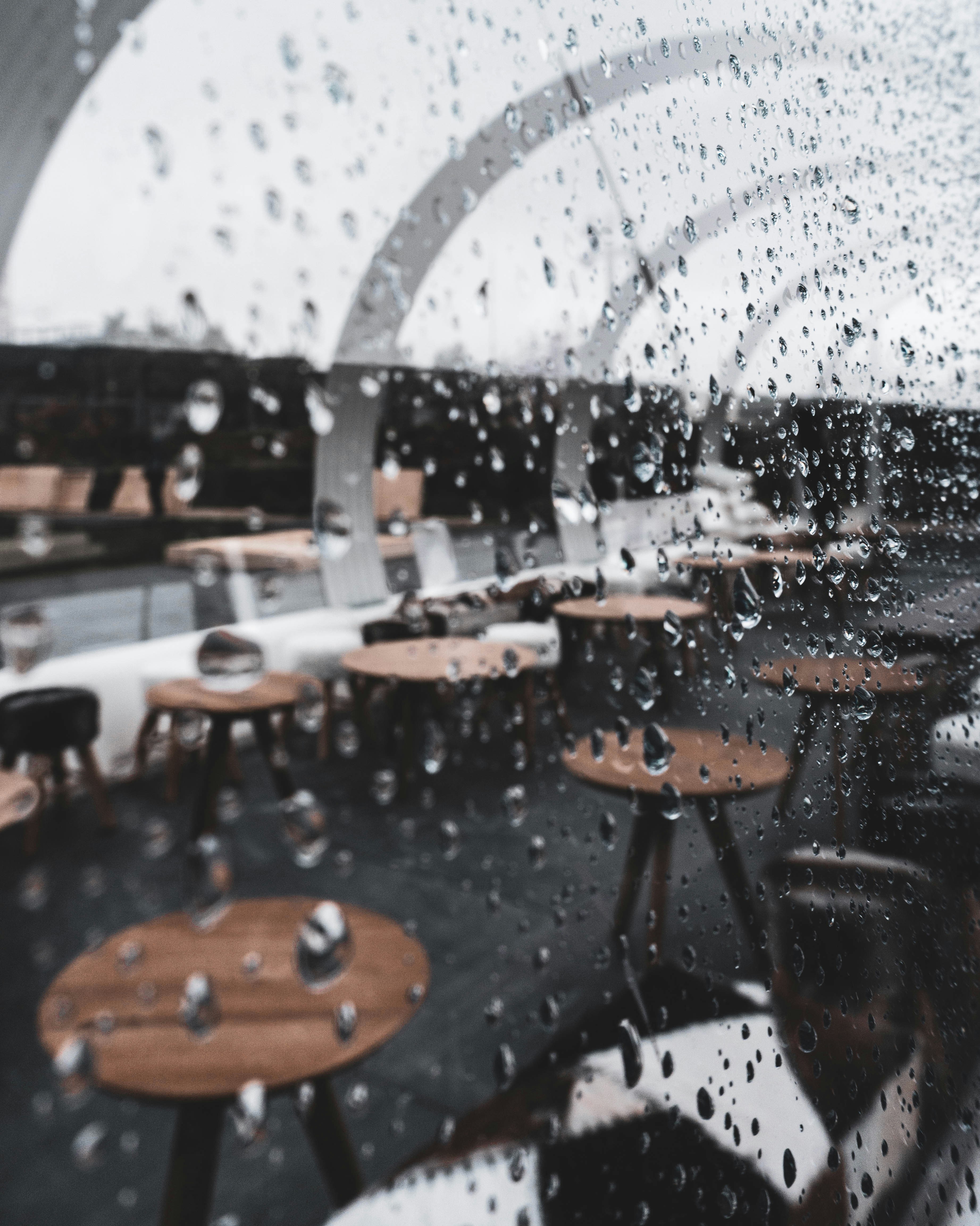 Close-up view through a rain-soaked window showcasing a serene café scene with wooden tables and blurred background elements. 