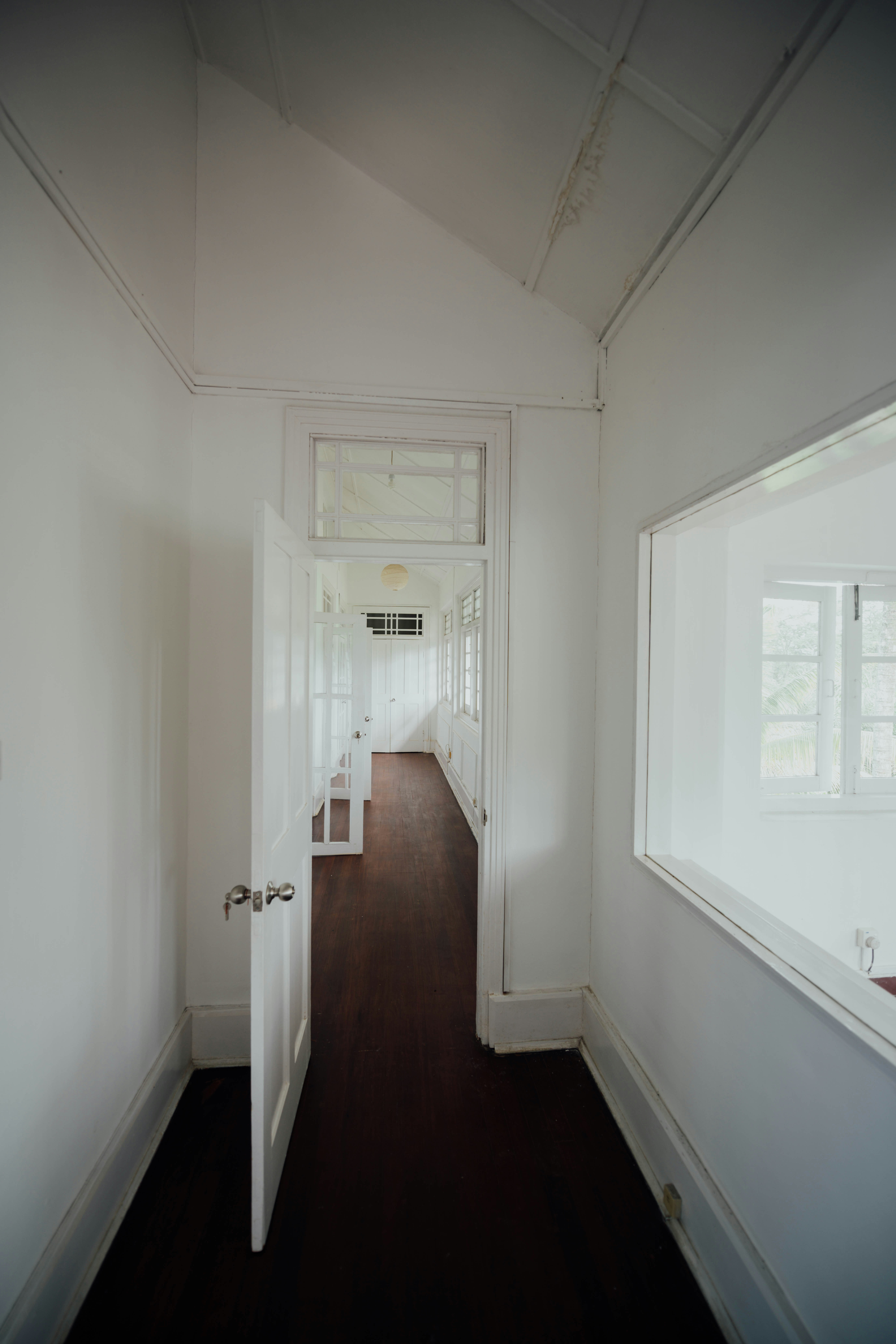 An open door leads into a serene hallway with white walls and wooden flooring, inviting exploration. Natural light filters through the windows, enhancing the tranquil atmosphere.