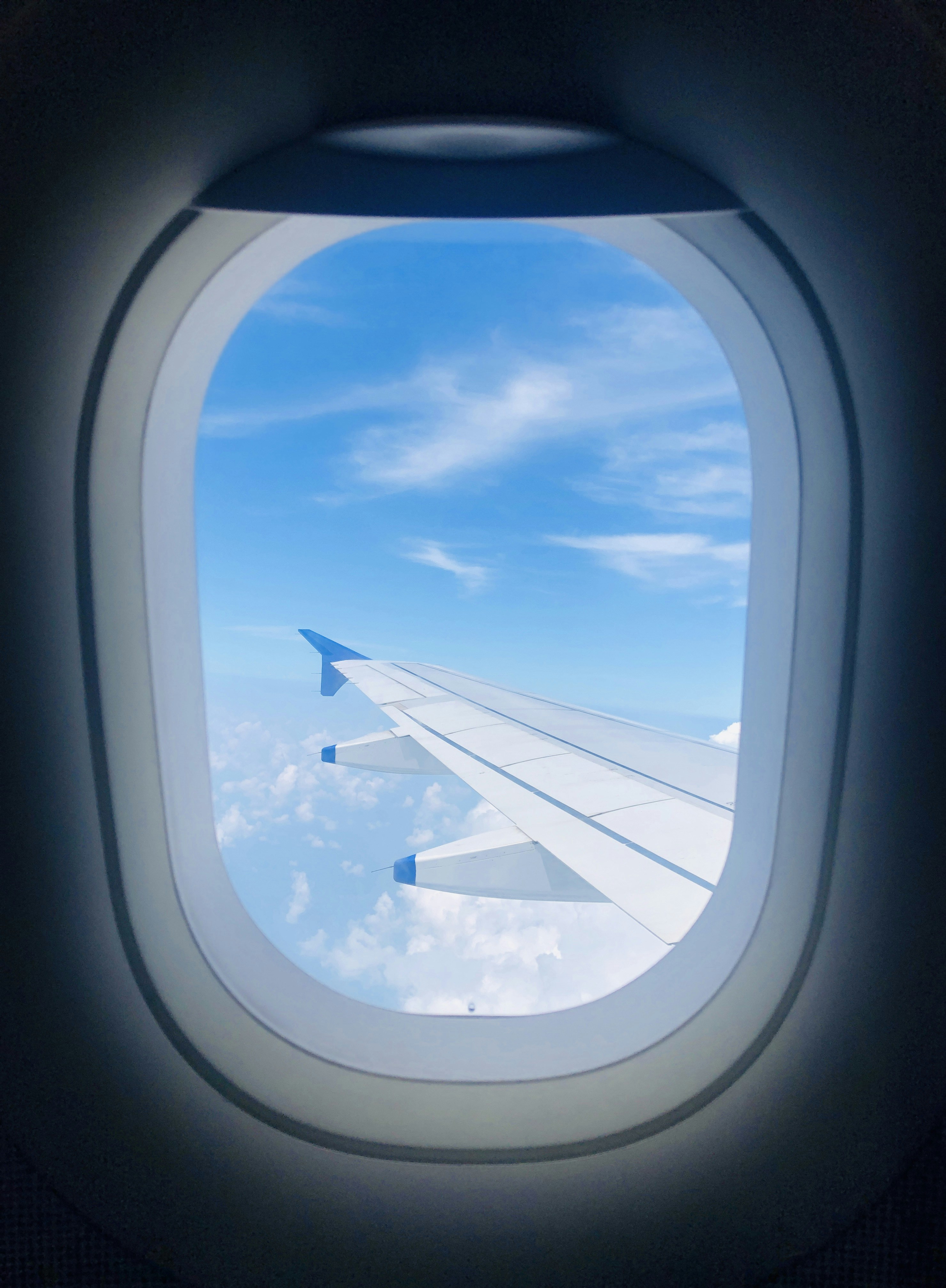 View from an airplane window showcasing the wing against a backdrop of clear blue sky and fluffy clouds.