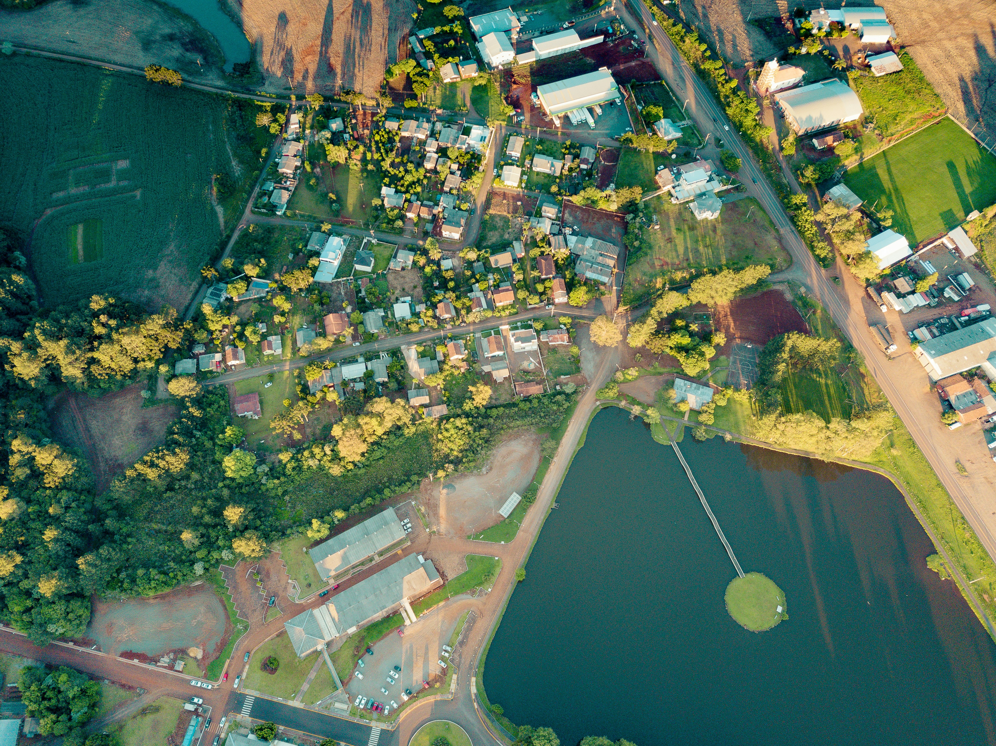 Aerial view of a suburban landscape with tree-lined streets, small lakes, and residential buildings bathed in warm light.