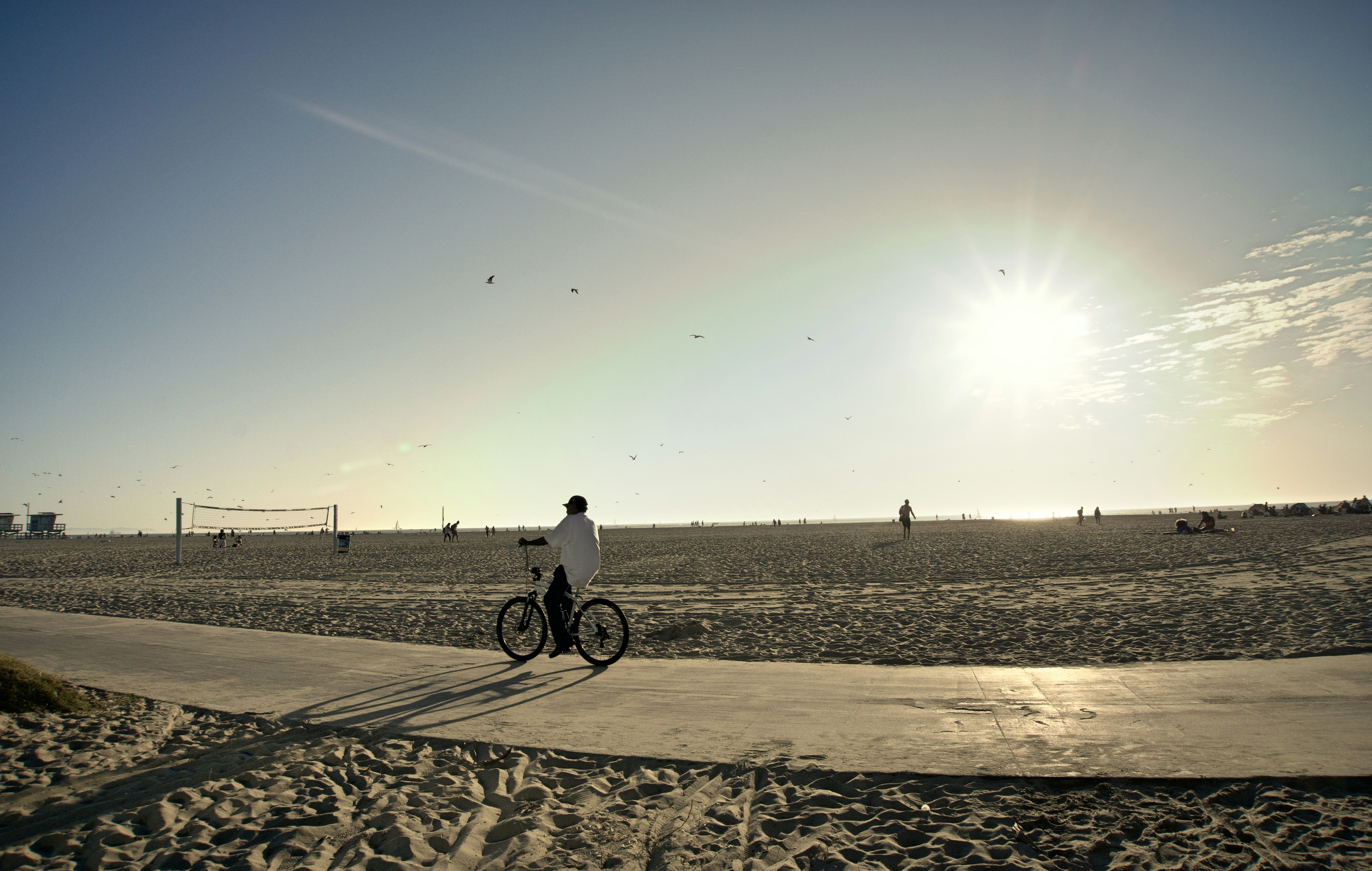 Cyclist on a Sunlit Beach Boardwalk with Distant Silhouettes