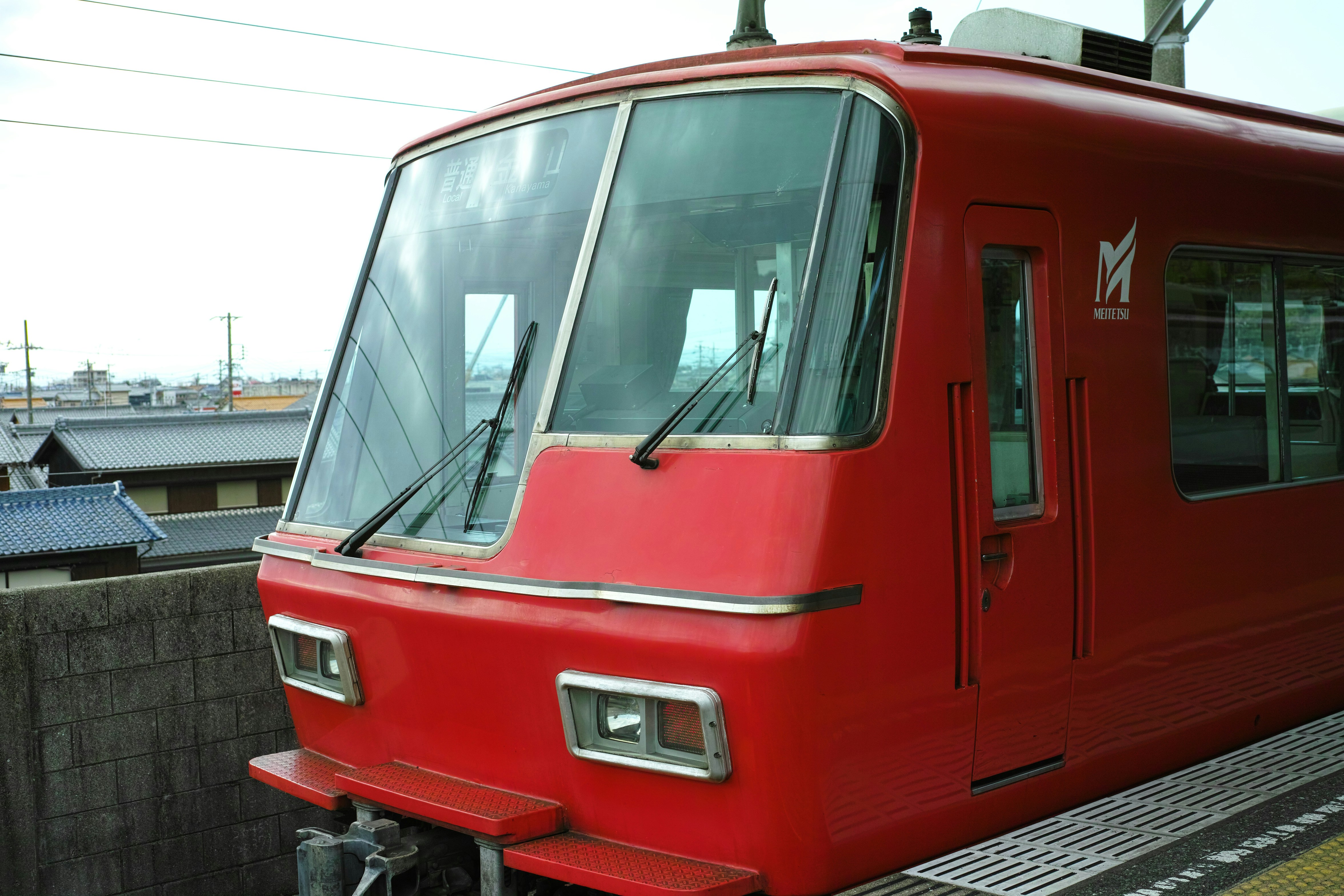 Red railcar at a station with a prominent front window and headlights, platform edge in the foreground.