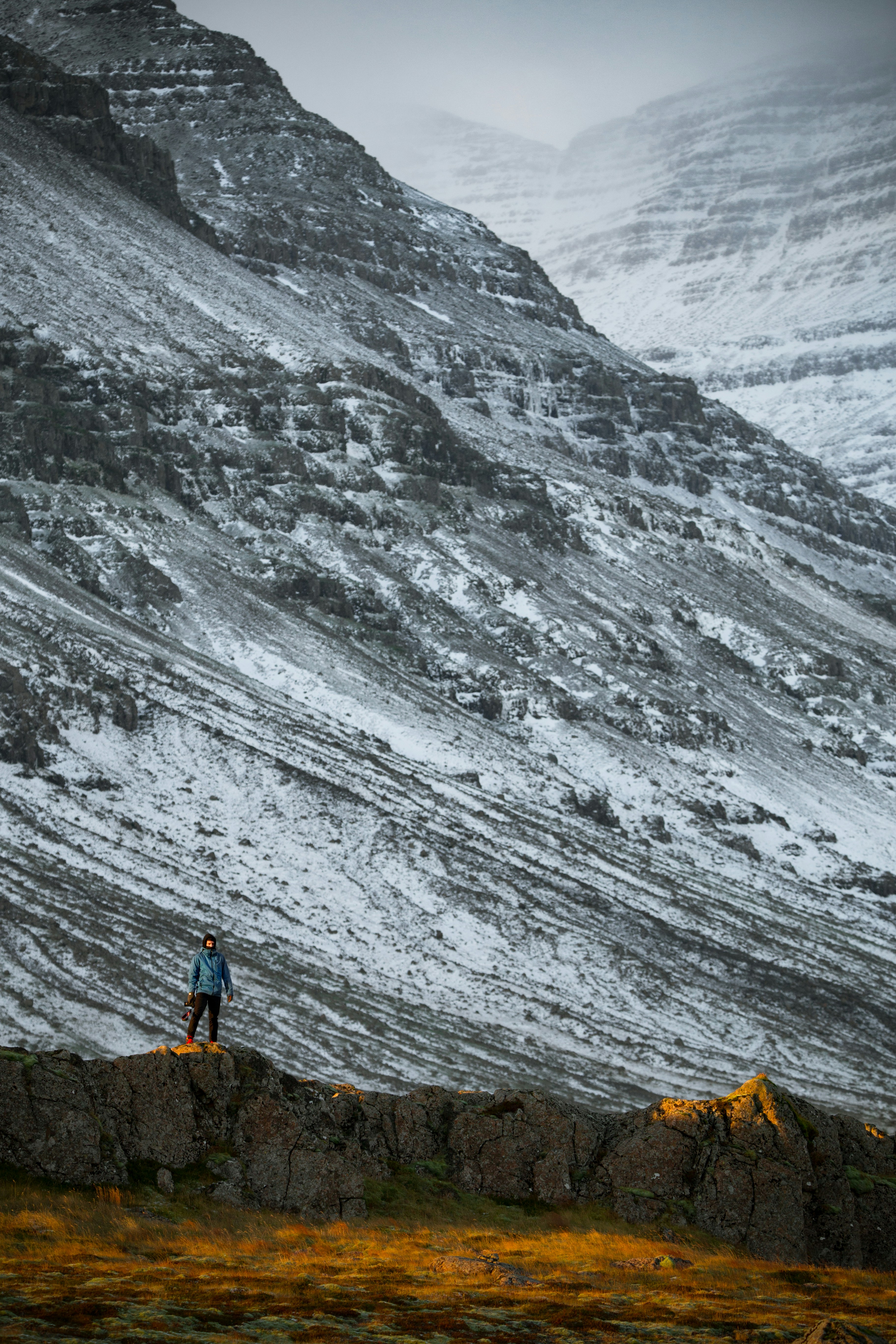  lone climber at the edge of a snow-dusted cliff under moody skies