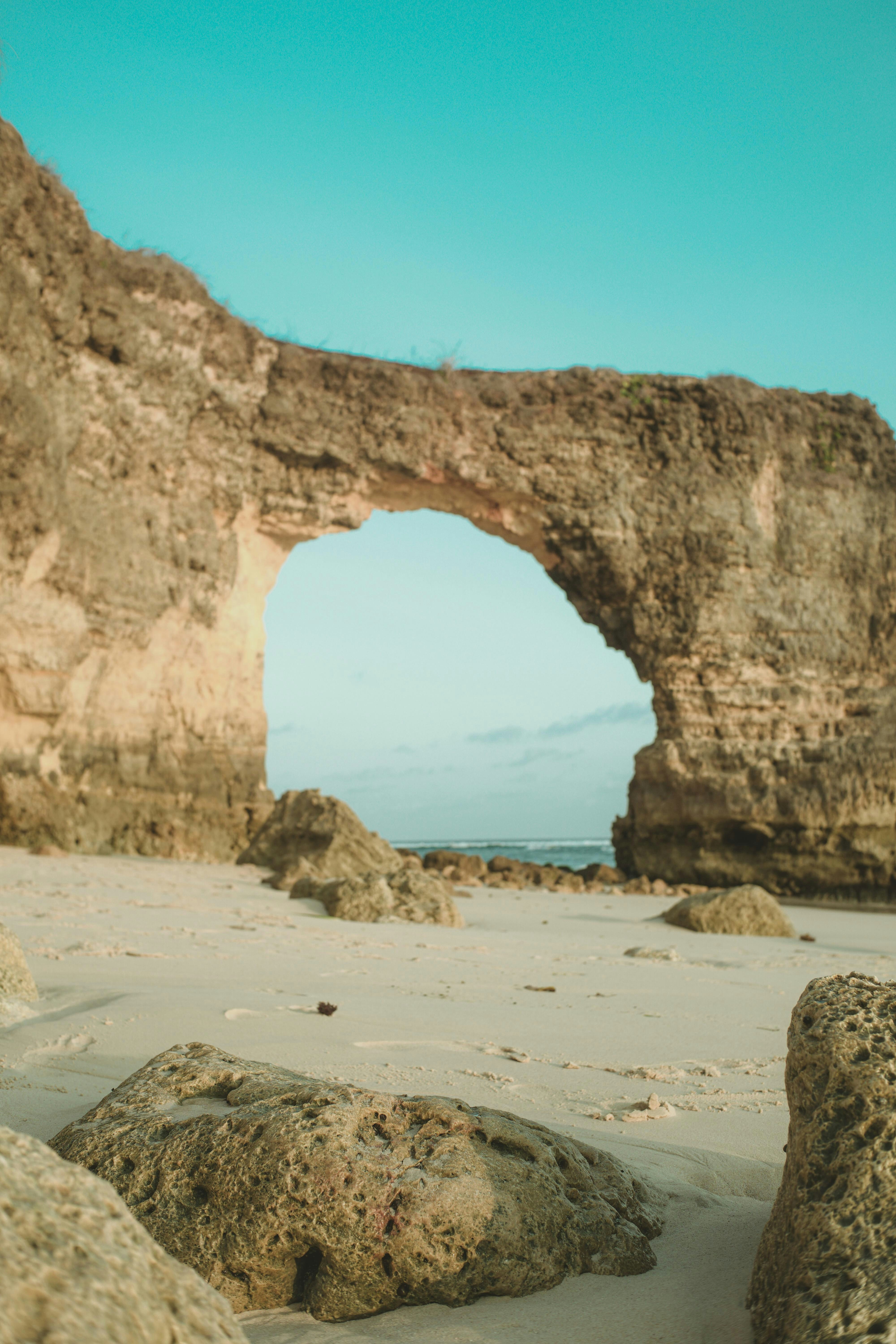 Natural rock arch rises over sandy shoreline under a clear blue sky.