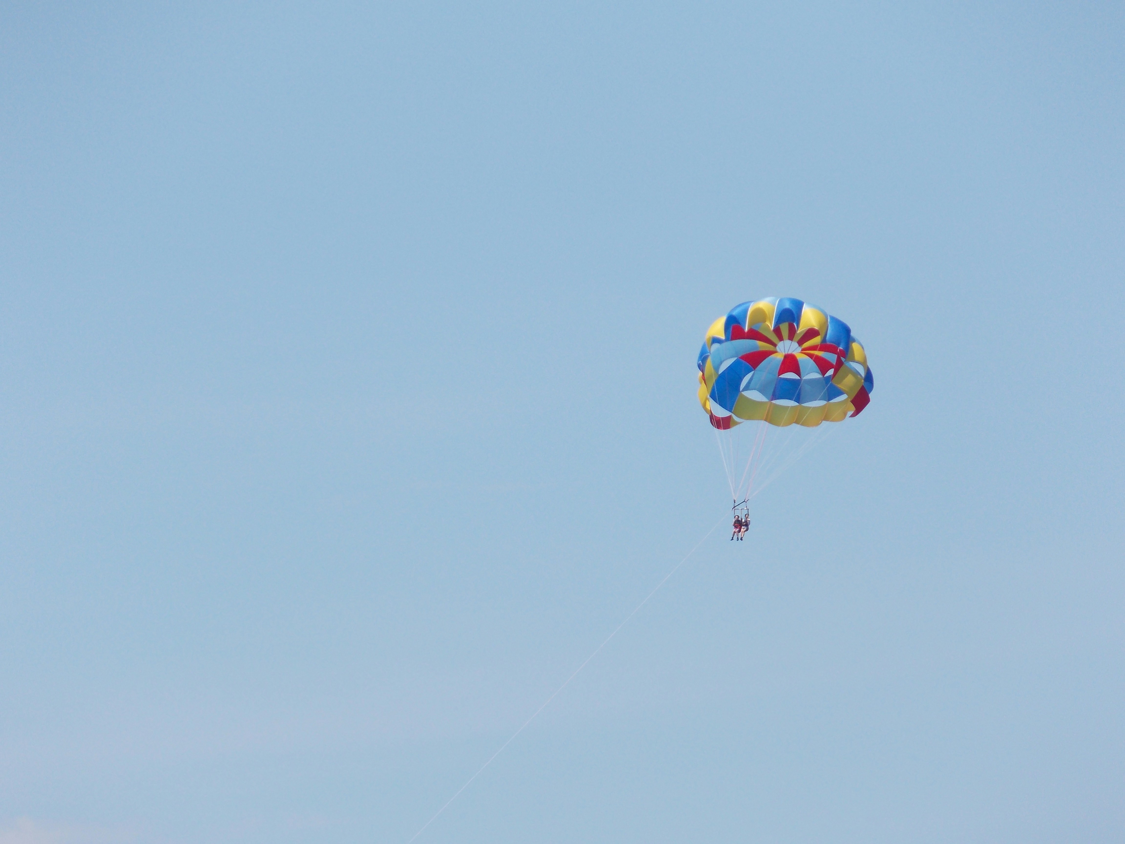 Colorful parasail against a clear blue sky with a single person suspended beneath.