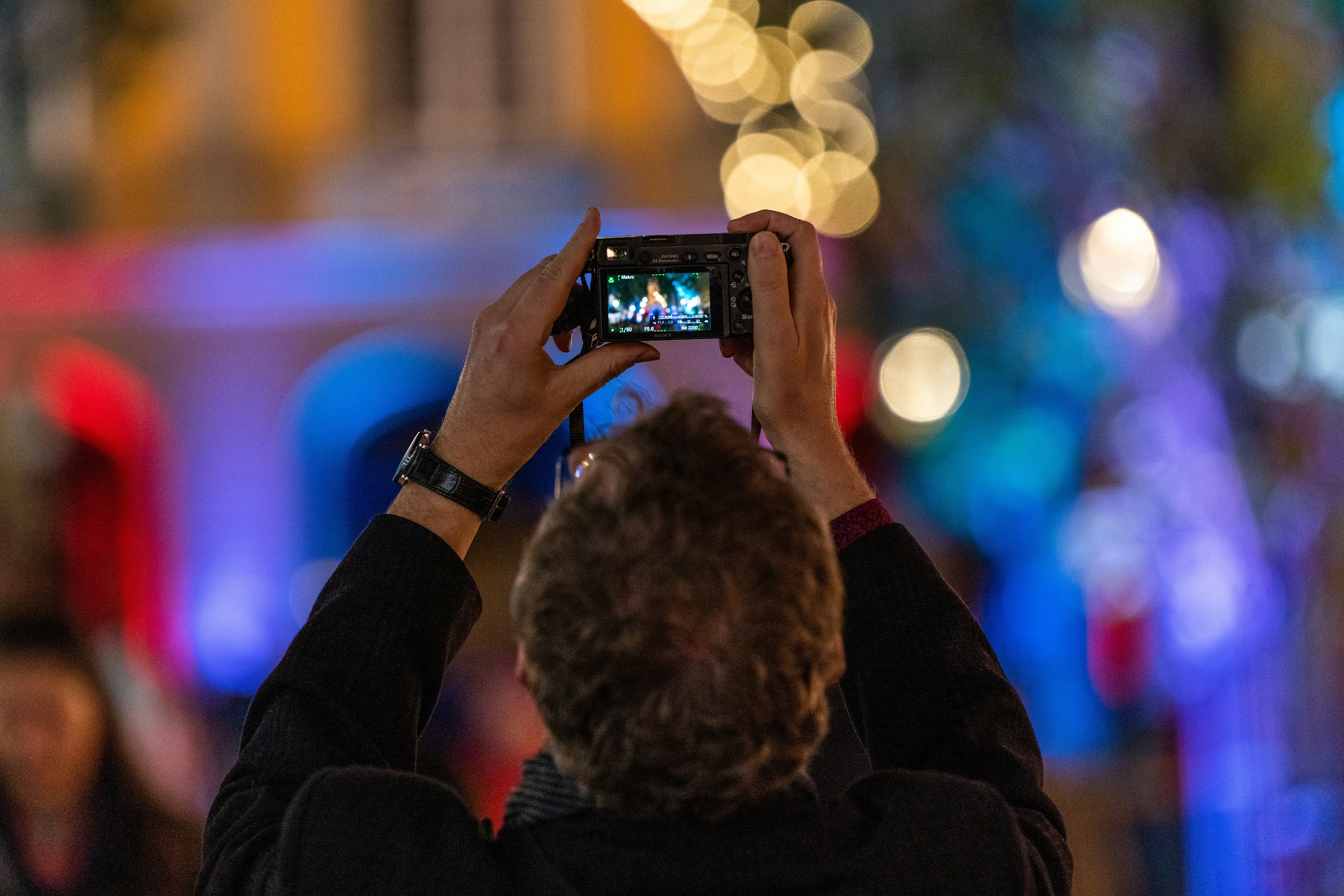 A person capturing a vibrant scene with a camera, surrounded by colorful lights and festive ambiance.