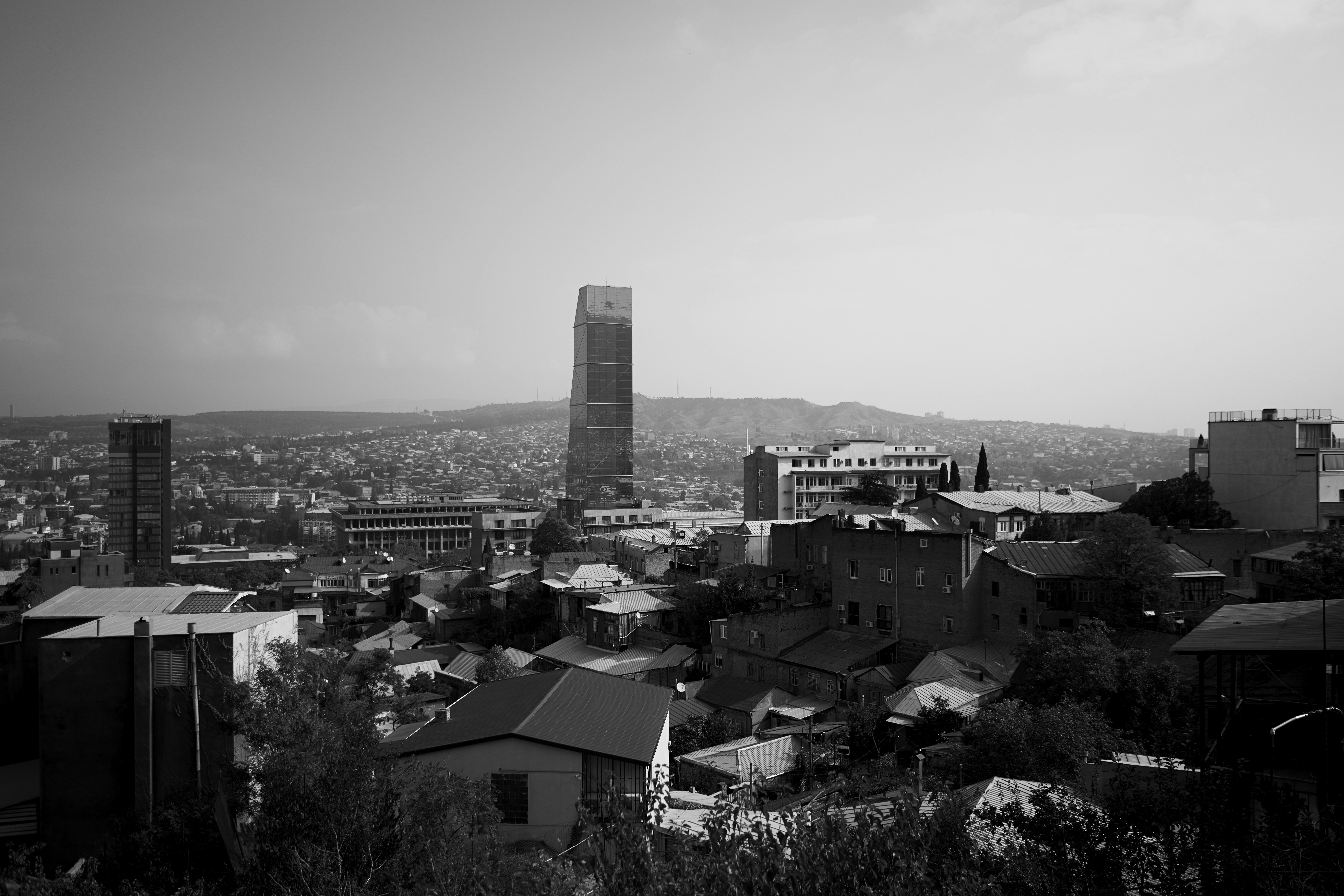 A panoramic view of a city skyline featuring a prominent tower amidst a sea of rooftops, captured in black and white. The scene conveys a sense of urban depth and architectural contrast.