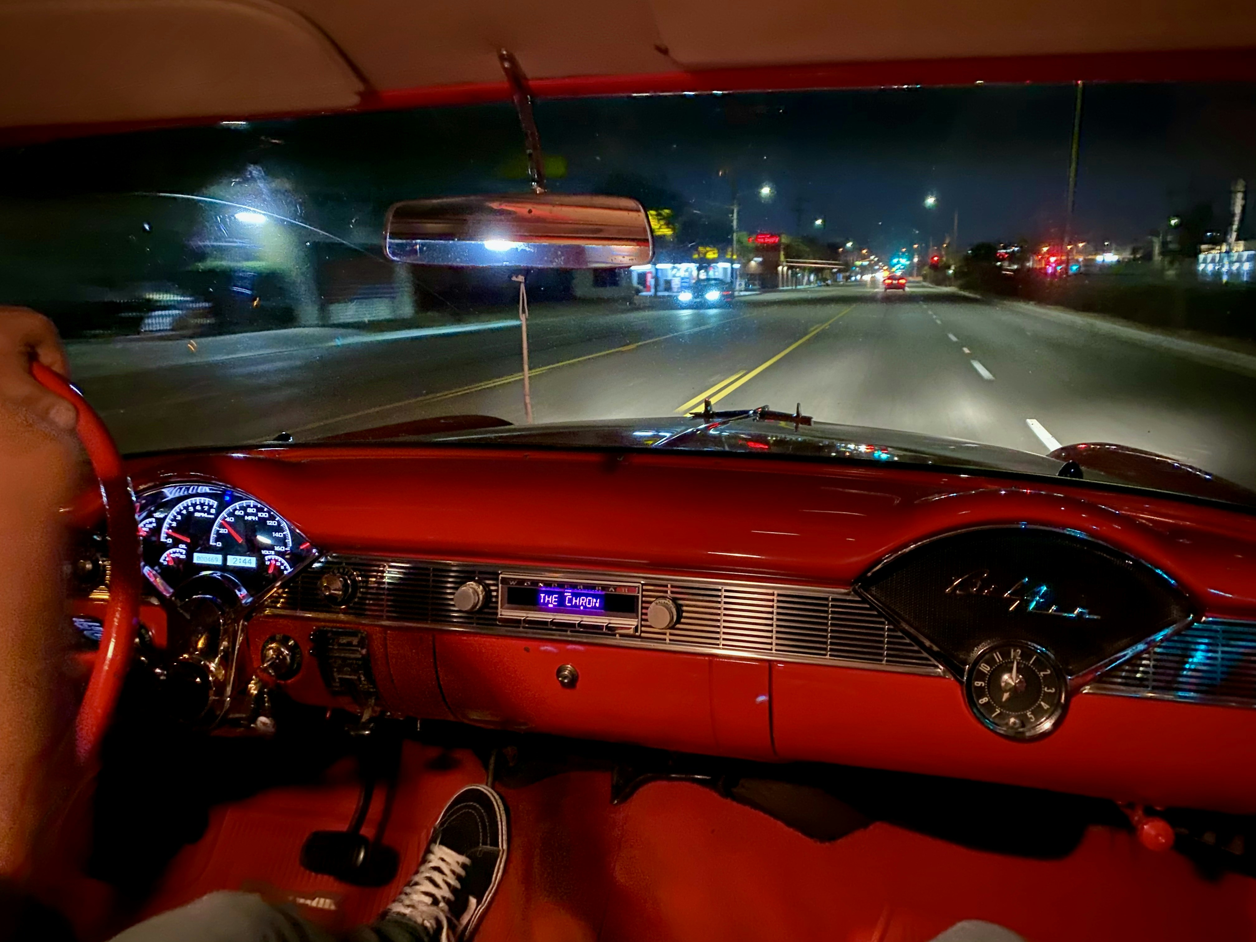 Vintage car interior with illuminated dashboard cruising a city road at night.
