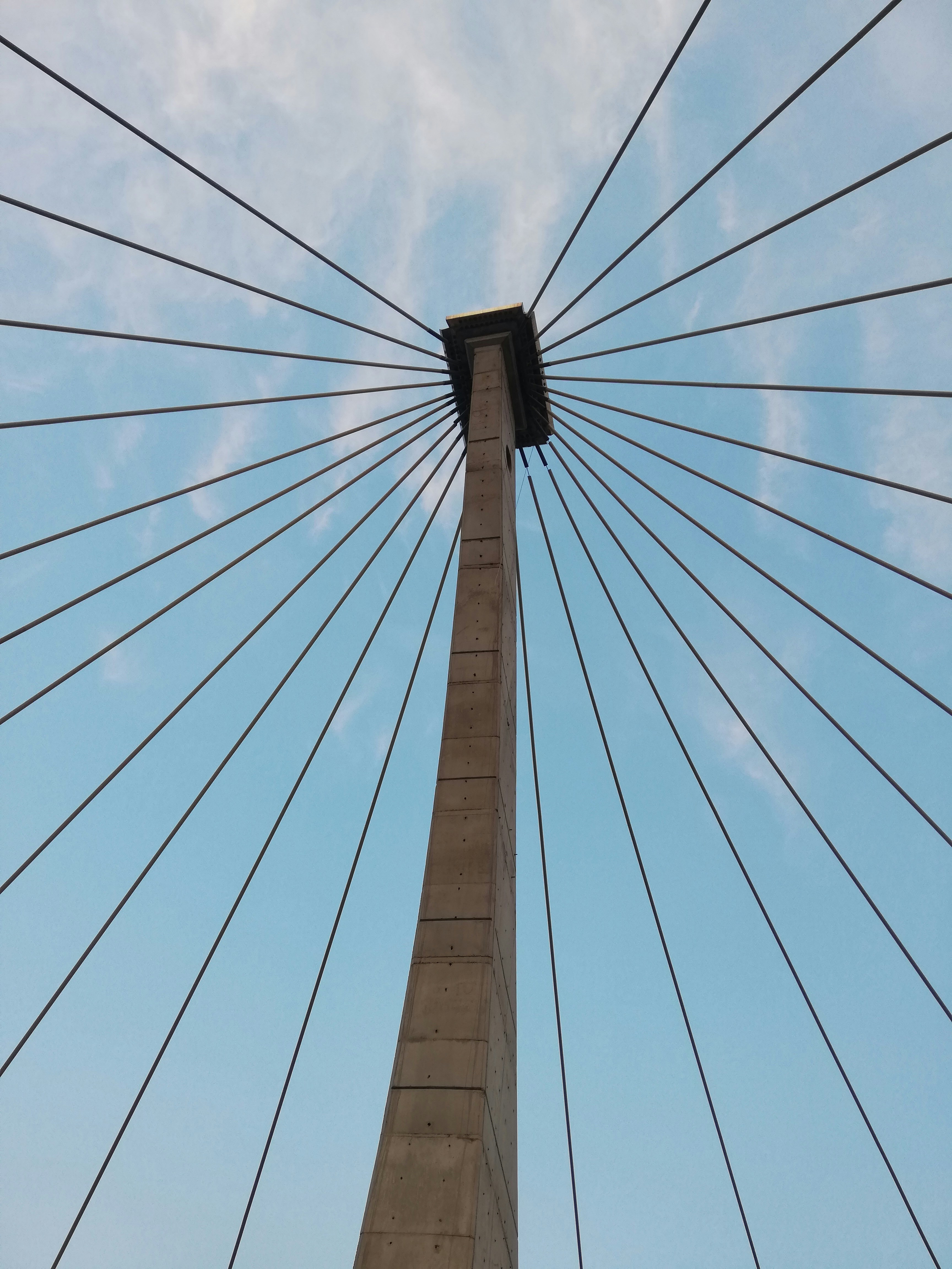 A towering concrete pillar with radiating cables against a soft blue sky, showcasing modern engineering aesthetics.