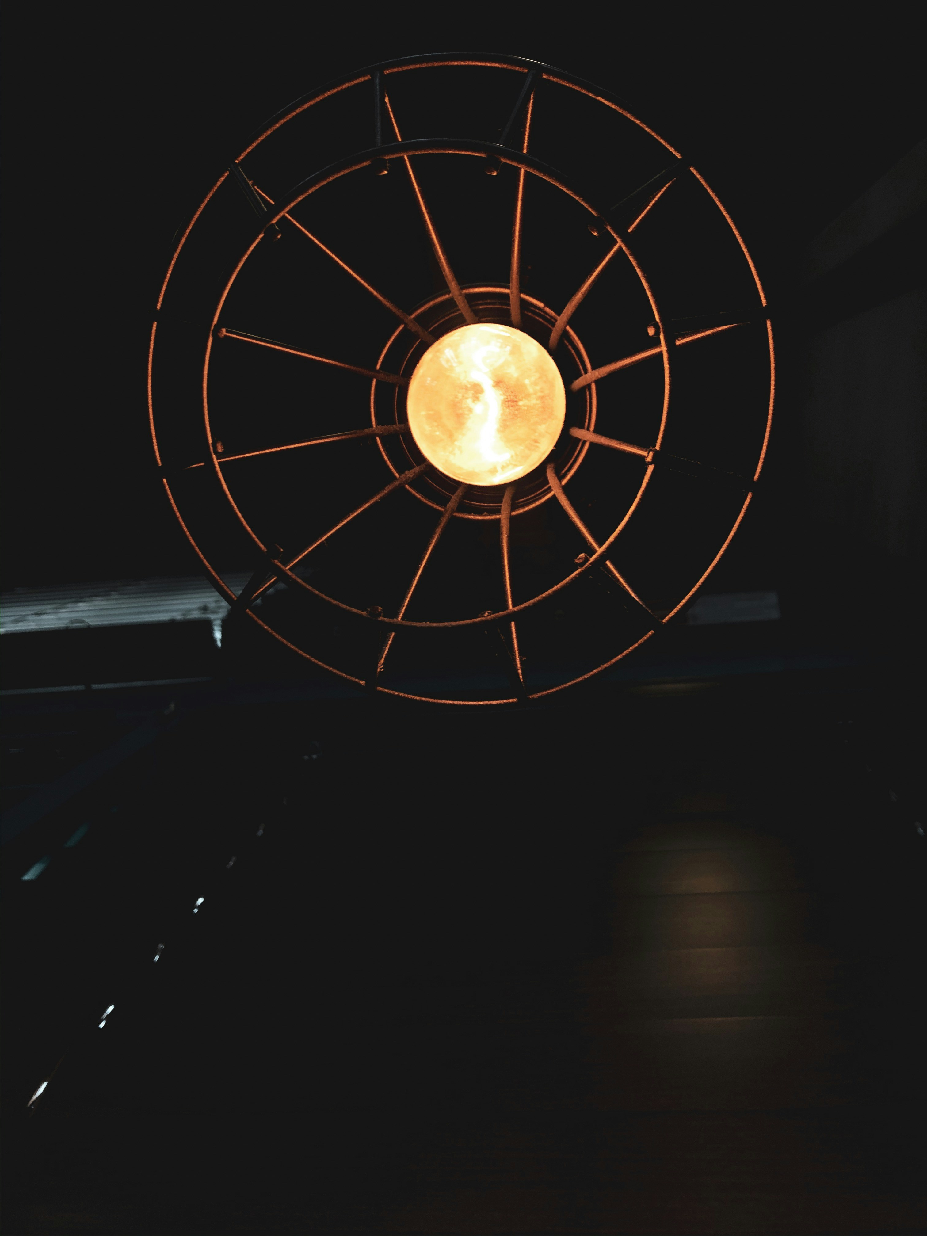 A circular light fixture with a wireframe design casts warm illumination against a dark background, creating a striking contrast.