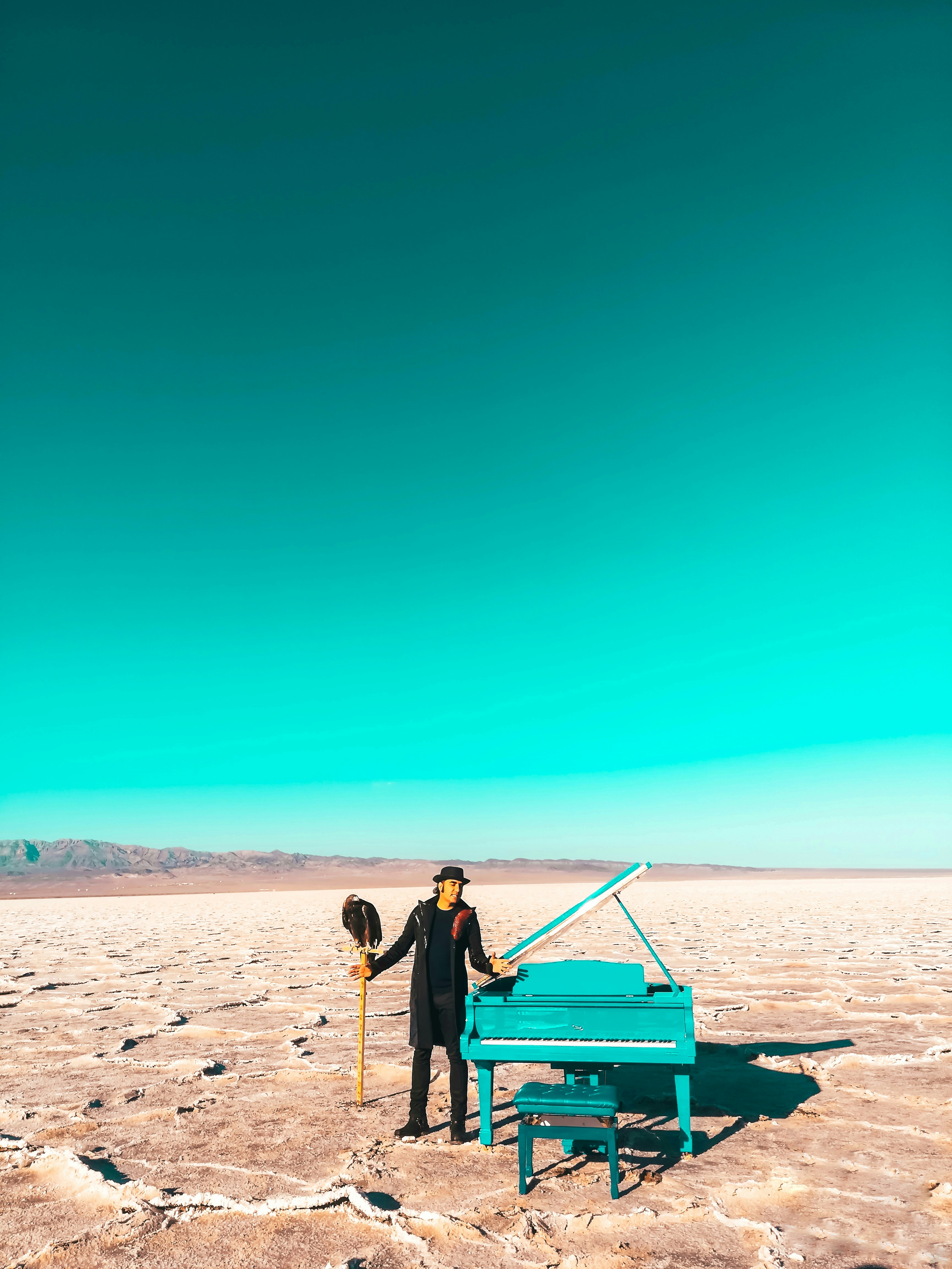 A Cyan Piano in a Salt Flat: Man with Staff and Teal Grand Piano under Surreal Sky