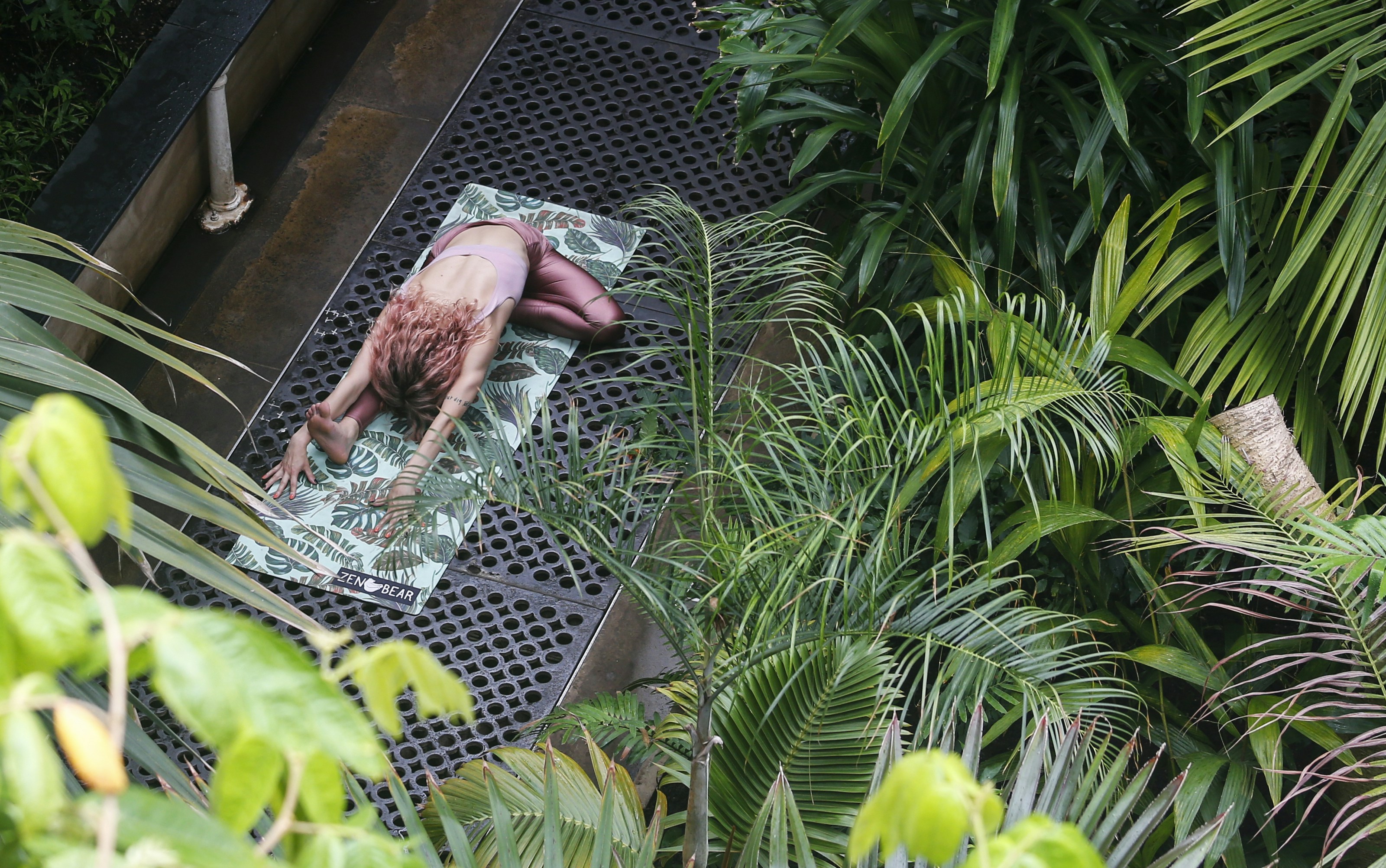 A person practicing yoga on a patterned mat, surrounded by lush greenery in a tranquil setting. The scene captures a moment of peace and connection with nature.