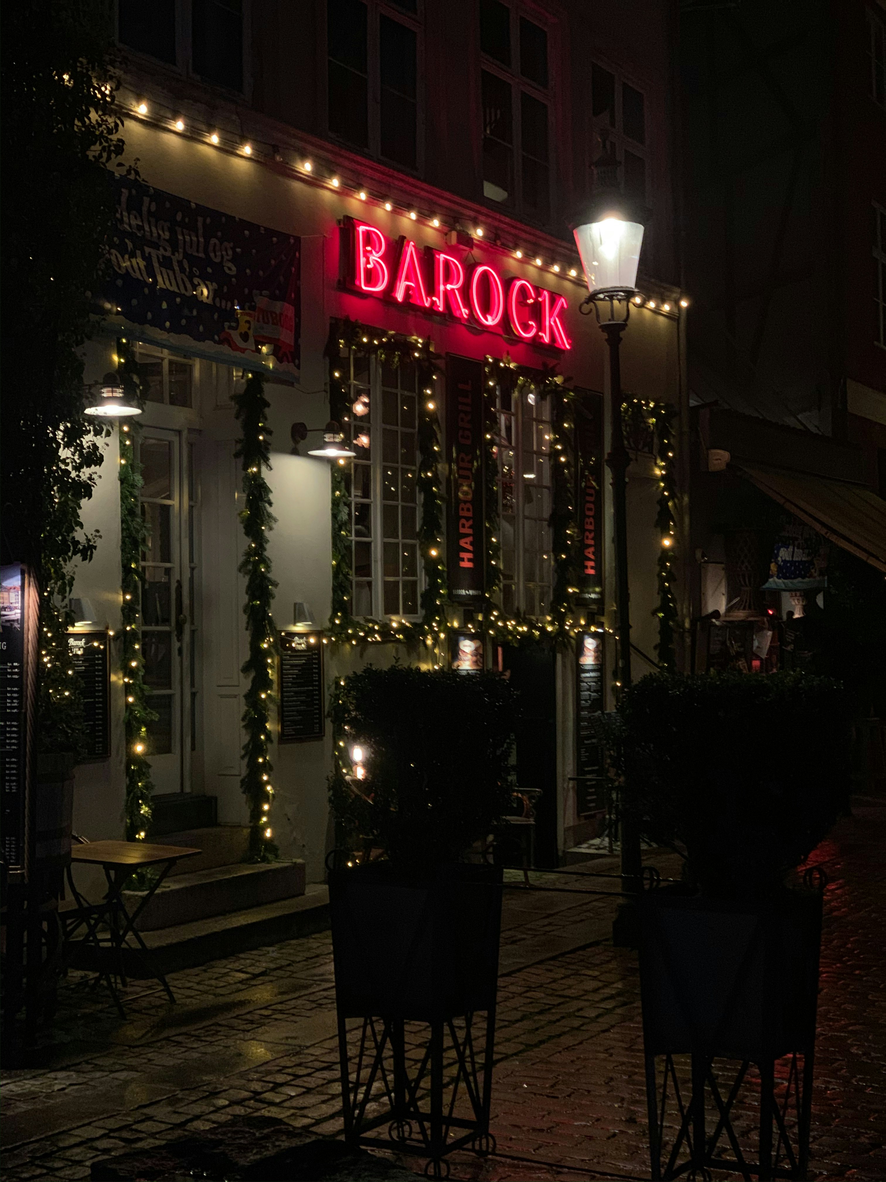 Charming restaurant adorned with vibrant neon signage and festive lights, creating a warm ambiance on a cobblestone street at night.