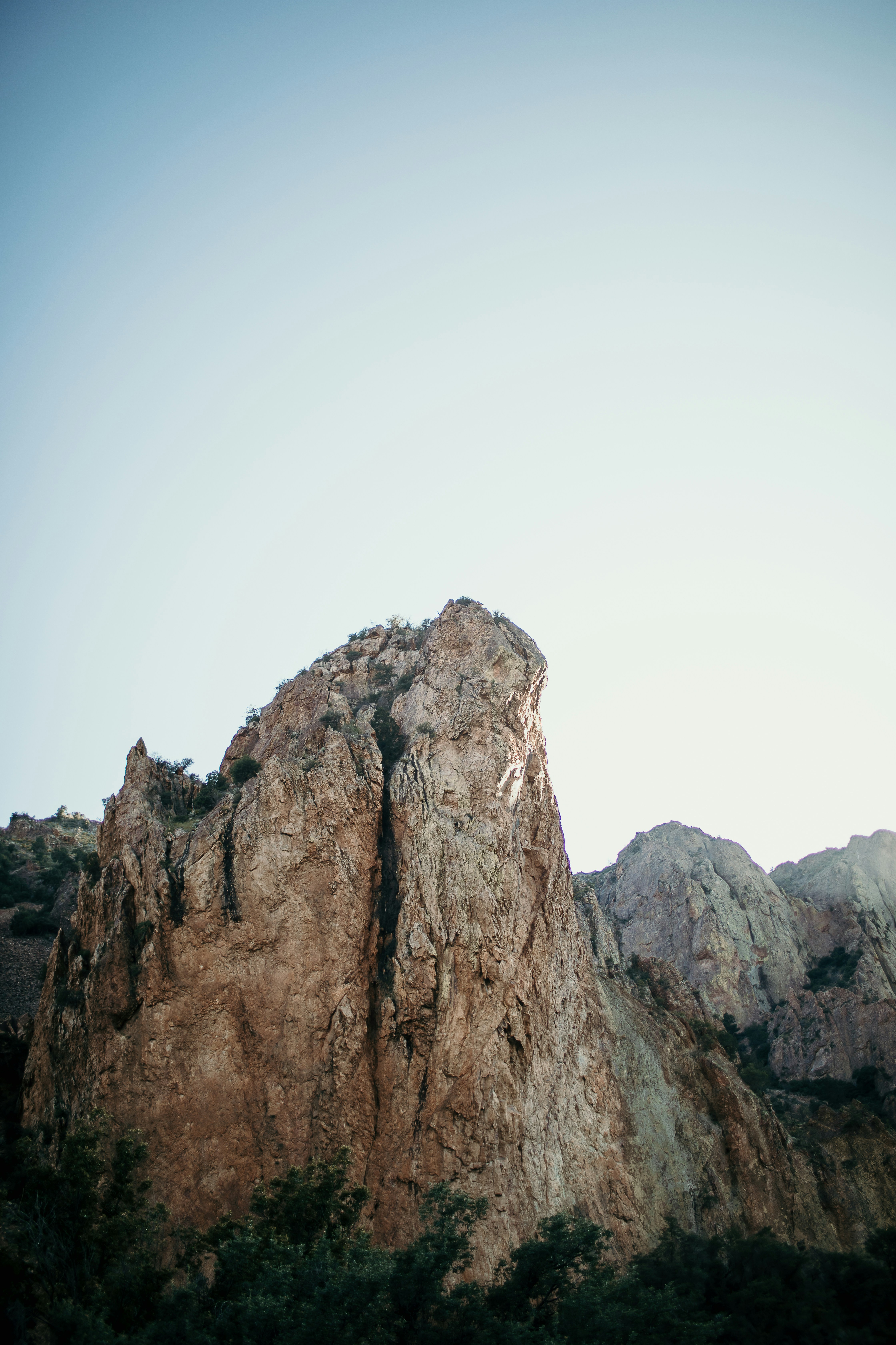 Majestic rock formation rising against a clear sky, surrounded by lush greenery. The sunlight casts subtle highlights on its rugged surface.
