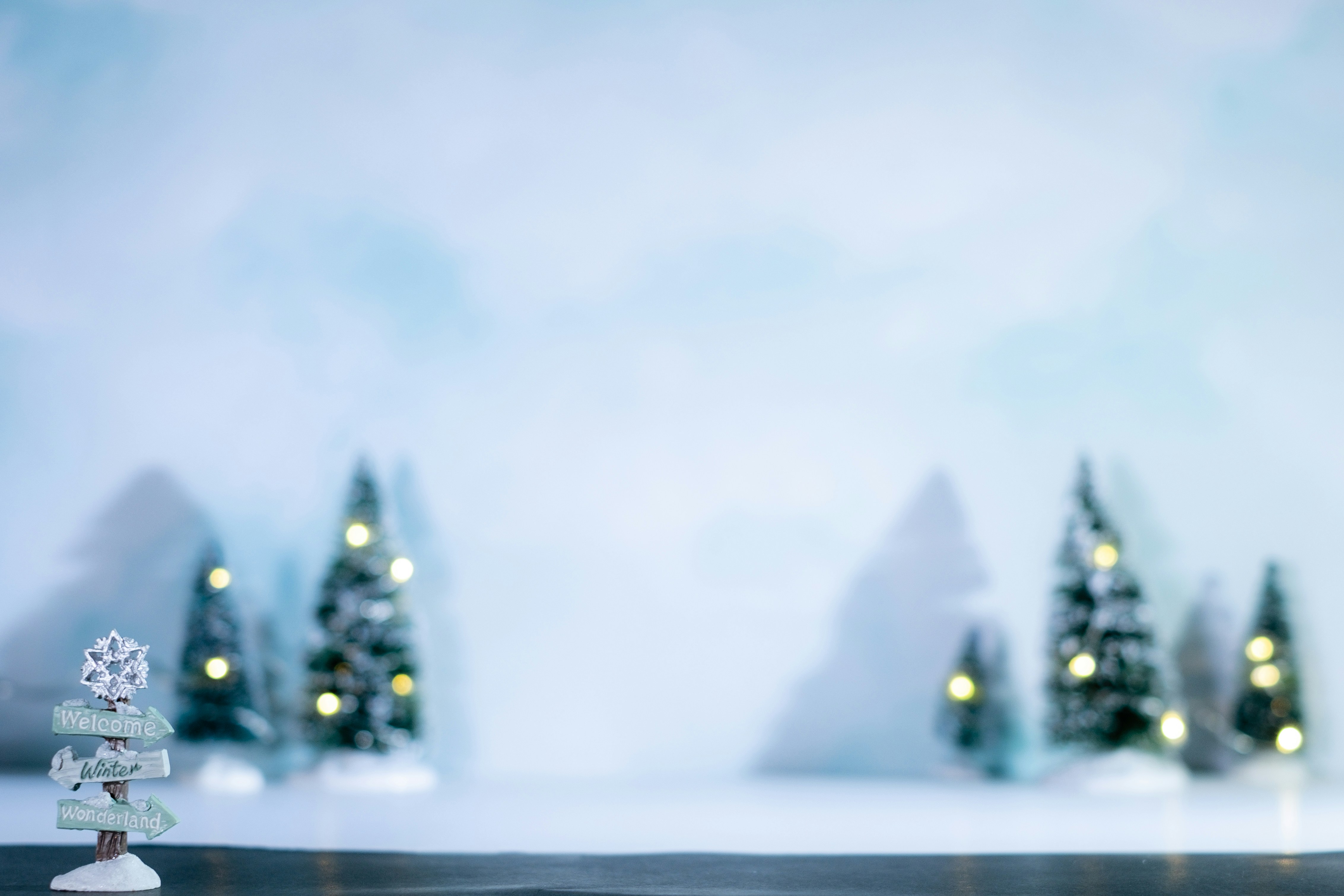 Miniature winter landscape featuring a decorative signpost and softly lit evergreen trees in the background.