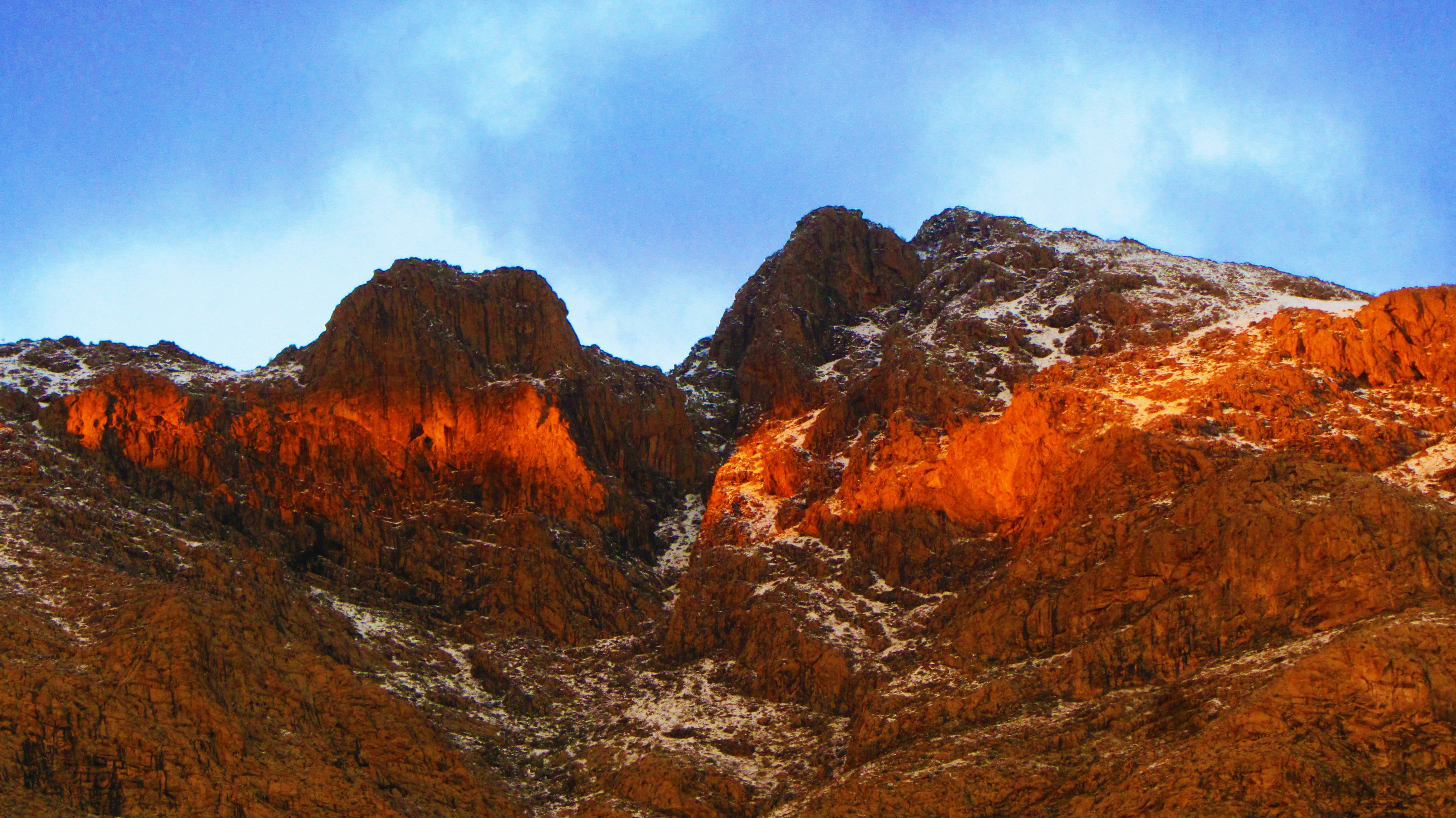 Sunlit mountain peaks with snow under a vivid blue sky.
