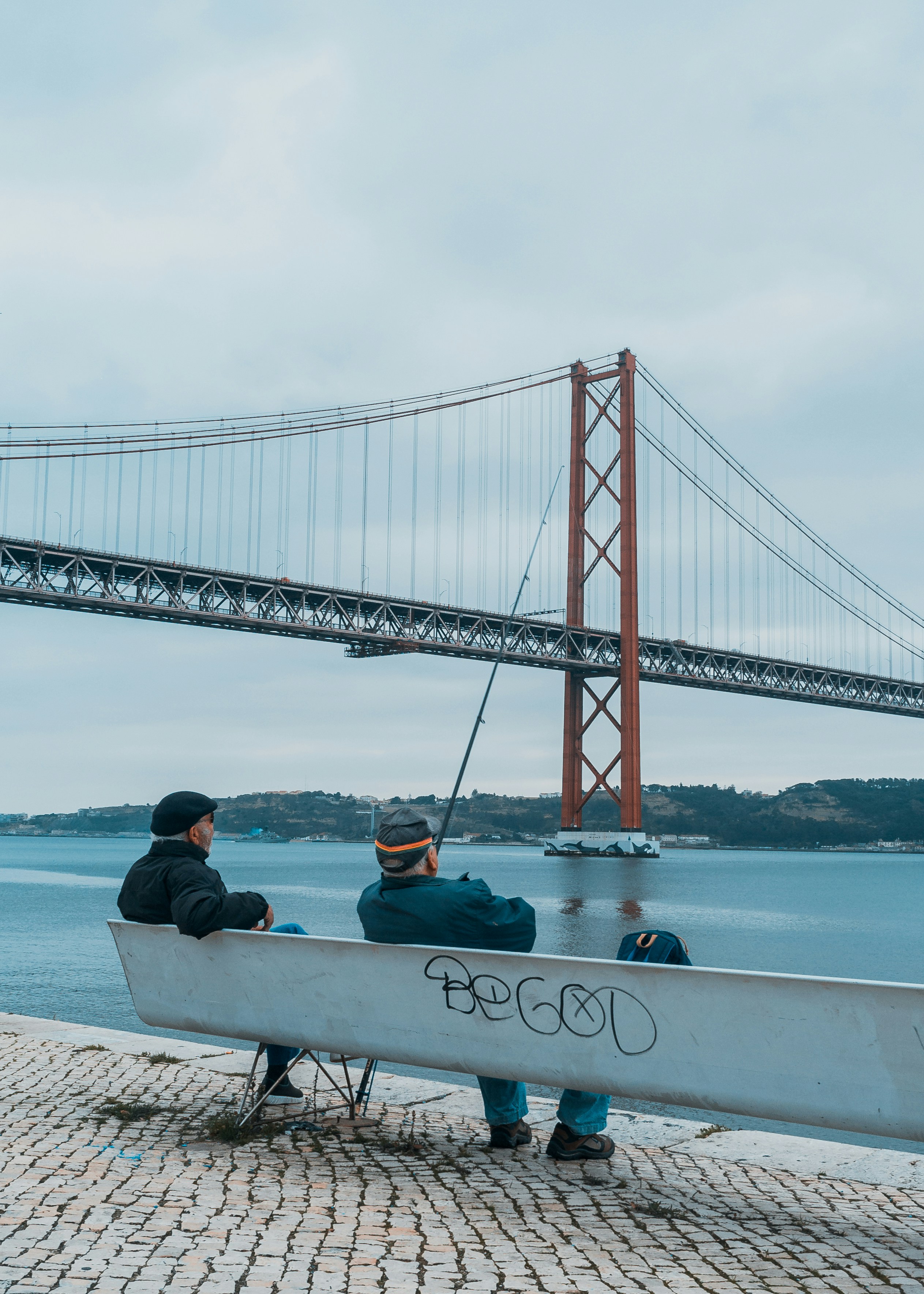 Lisbon bridge 25 de Abril and two old men fishing on the River Tejo.