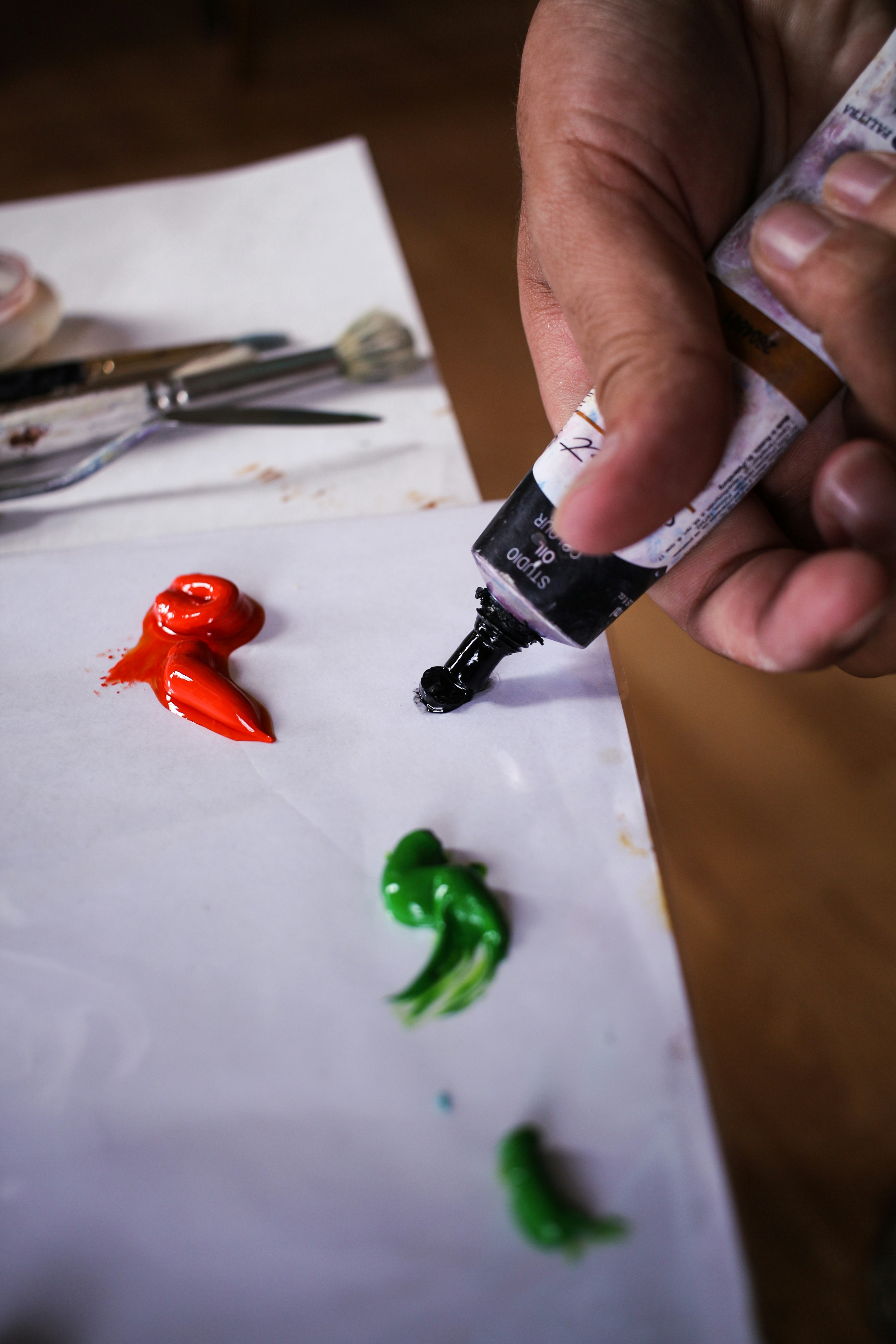 Artist's hand dispensing black paint onto a palette alongside vibrant red and green hues. The scene captures the essence of artistic expression.