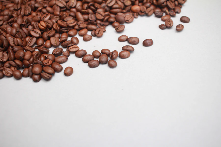 A spread of roasted coffee beans scattered across a clean white background, with dense clusters along the top and left edges. A few beans trail into the open space below.