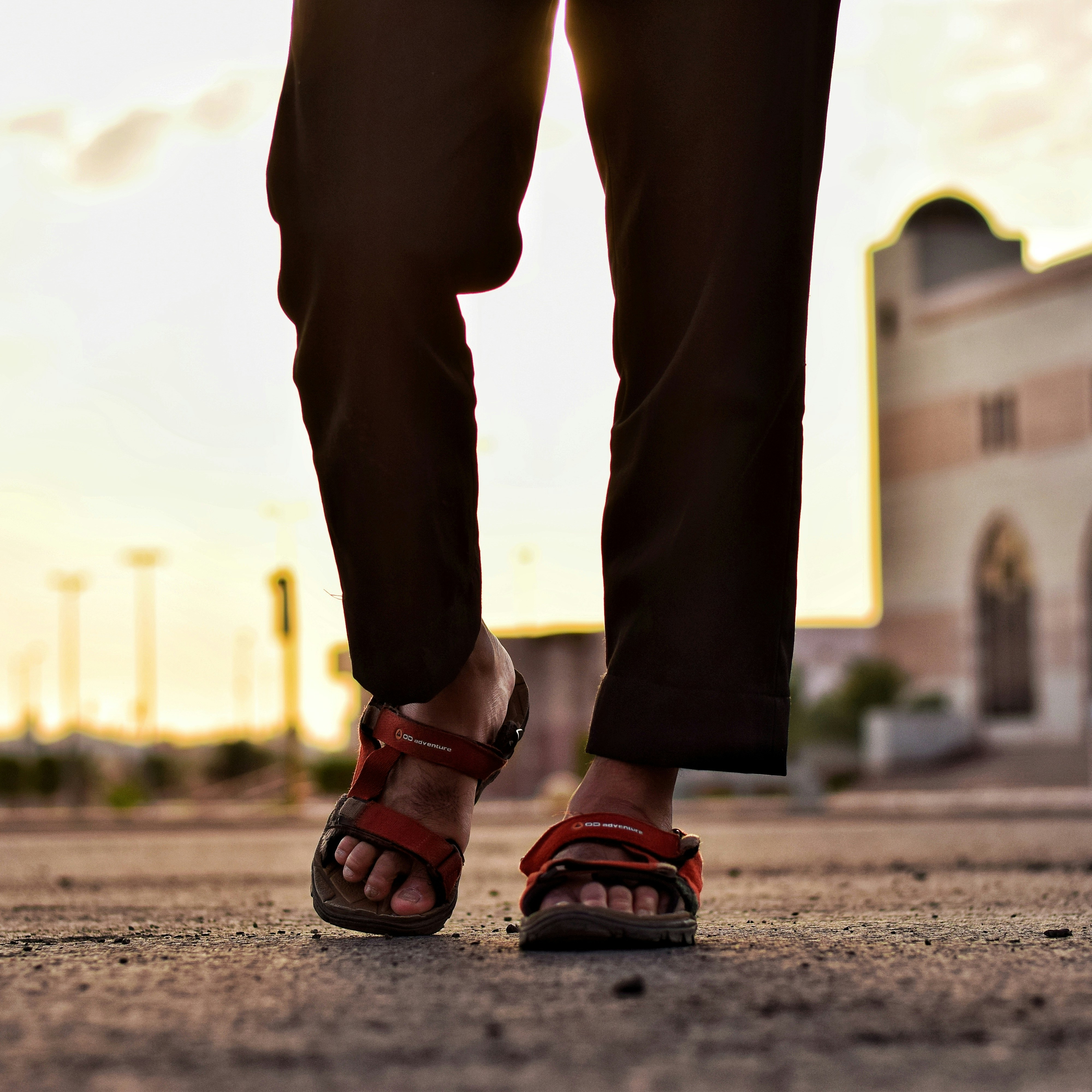 Sunset Steps: Ground-Level Portrait of Sandaled Feet Moving Toward a Backlit Arch