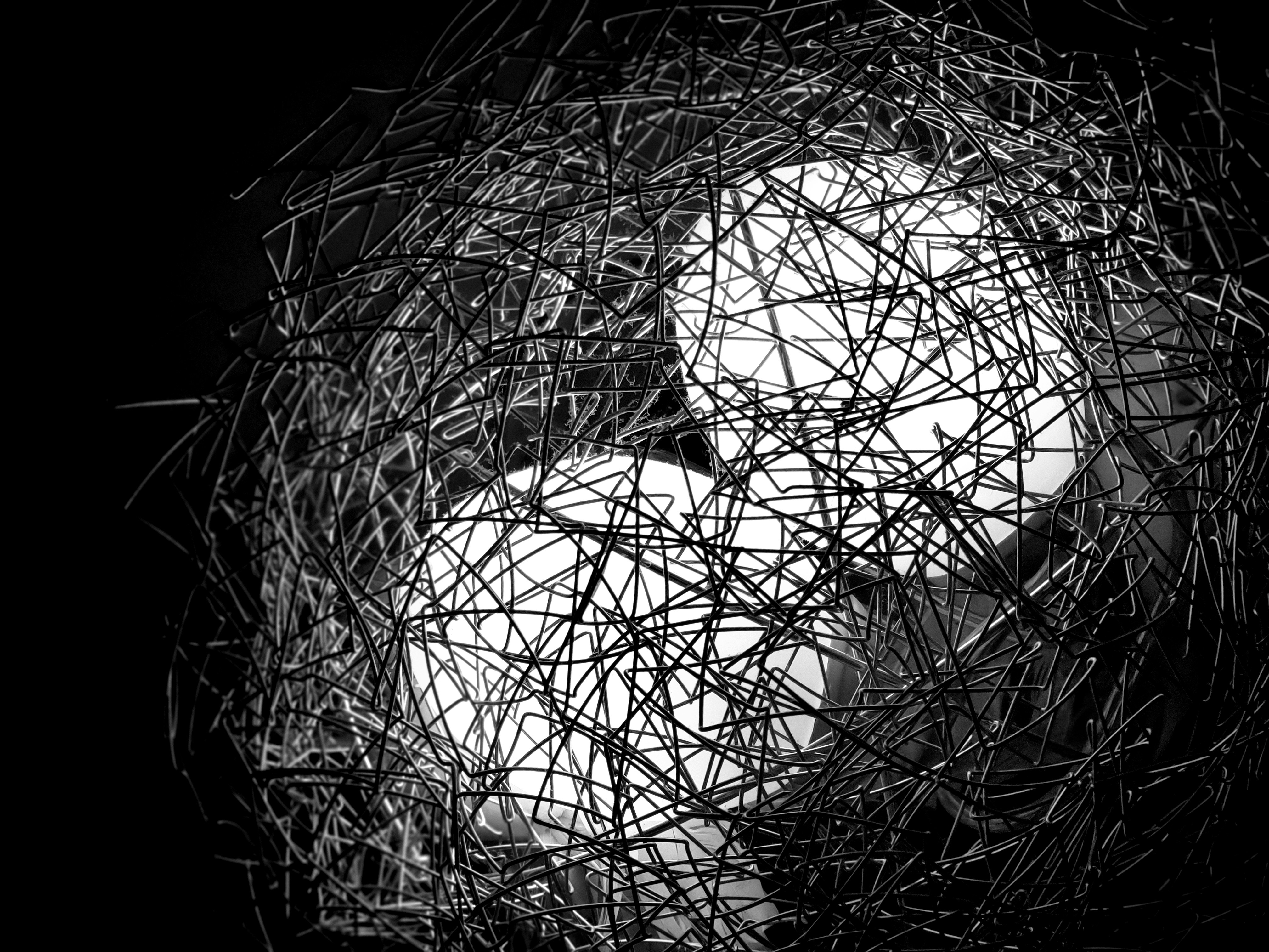 High-contrast black-and-white photograph of a dense tangle of wires forming two bright orbs, creating an abstract sculptural composition.