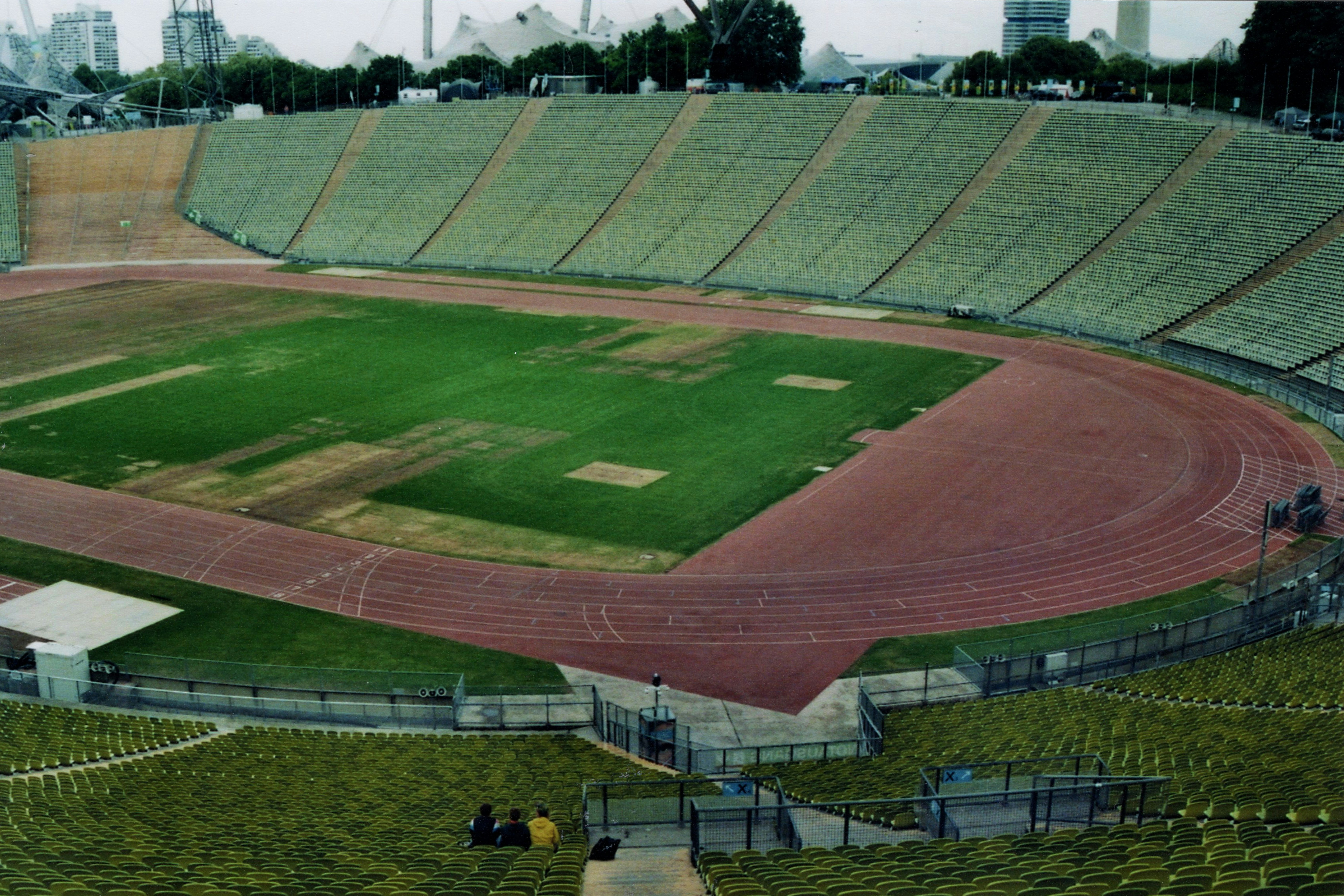 Expansive stadium with green field and surrounding track, empty spectator seats in foreground.