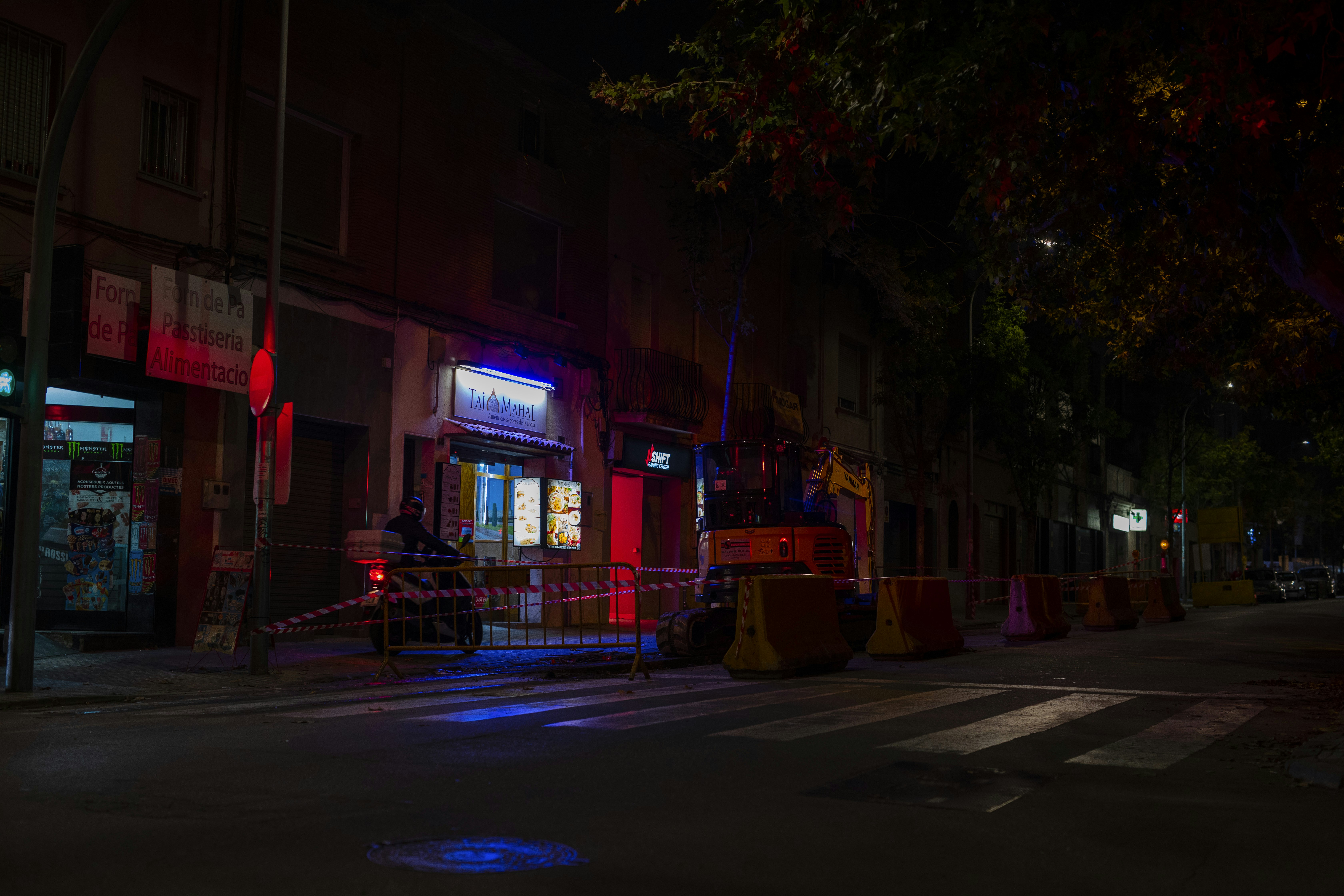 Dimly lit street with neon signs casting colorful glows on wet pavement at night.