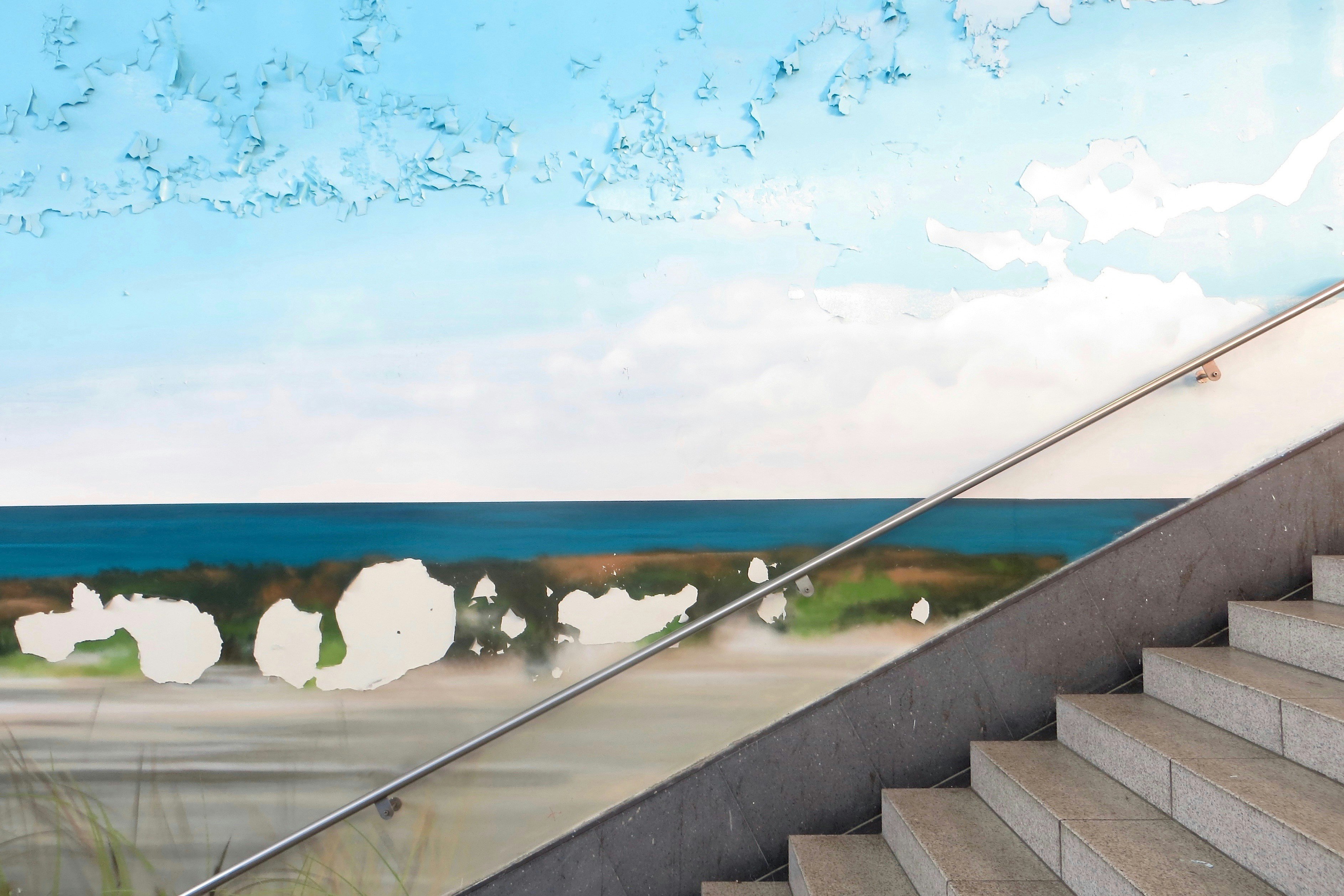Staircase leading upward with a mural depicting a serene beach scene, blending architecture and artistry. The mural features a vibrant sky and ocean view.
