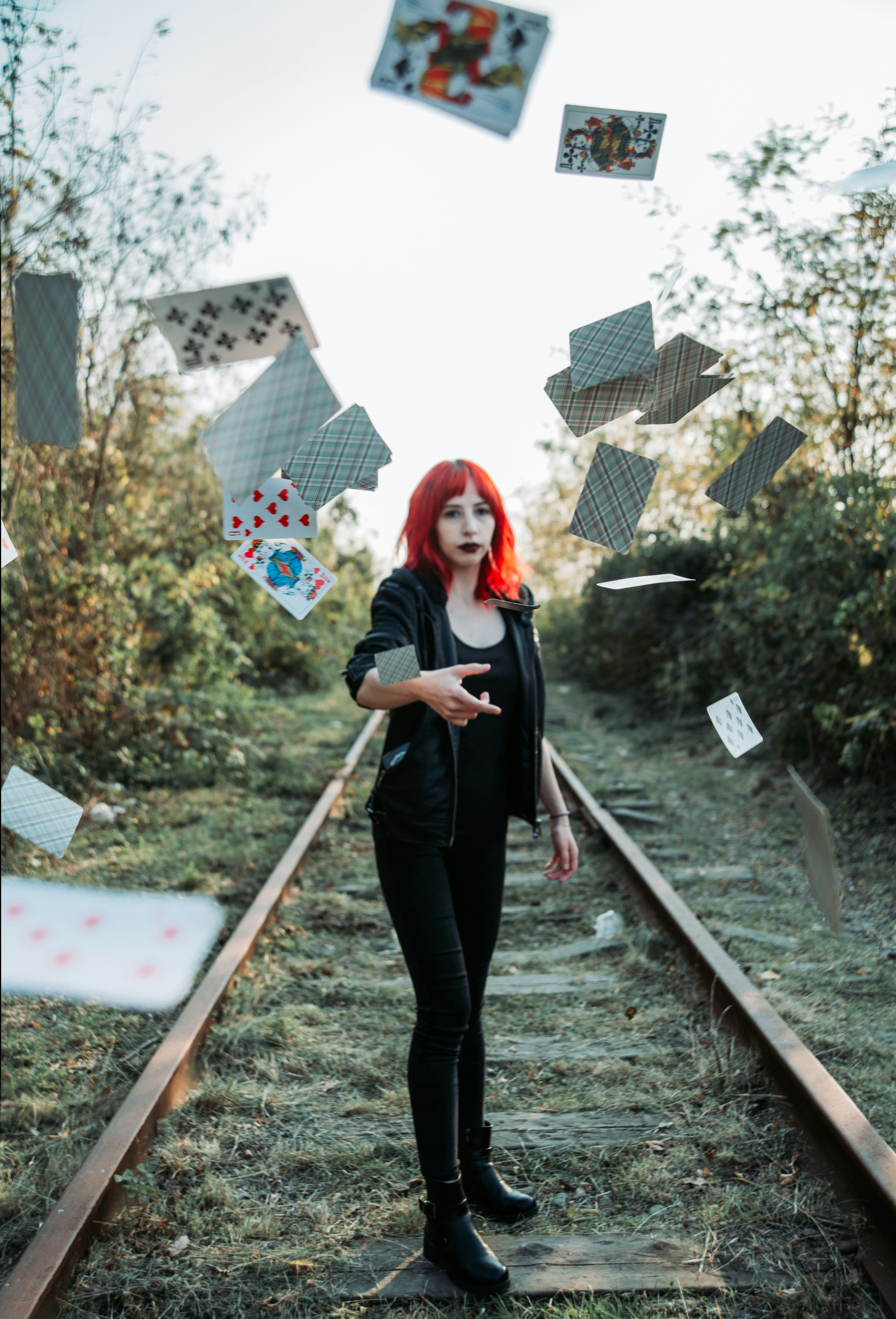 Woman with red hair wearing black jacket throwing cards while standing ...