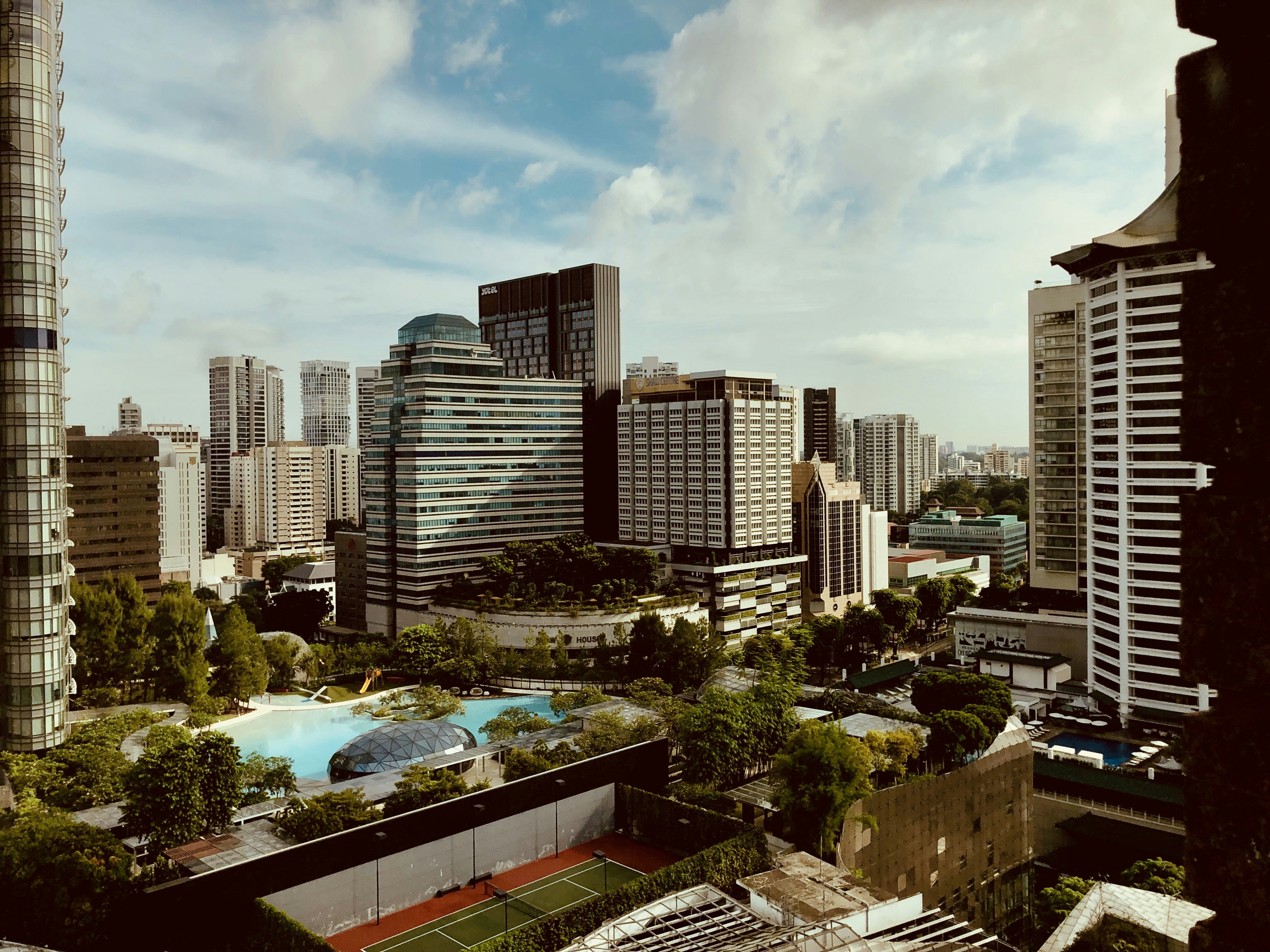 A vibrant cityscape featuring a lush park with a swimming pool, surrounded by towering skyscrapers and modern architecture.