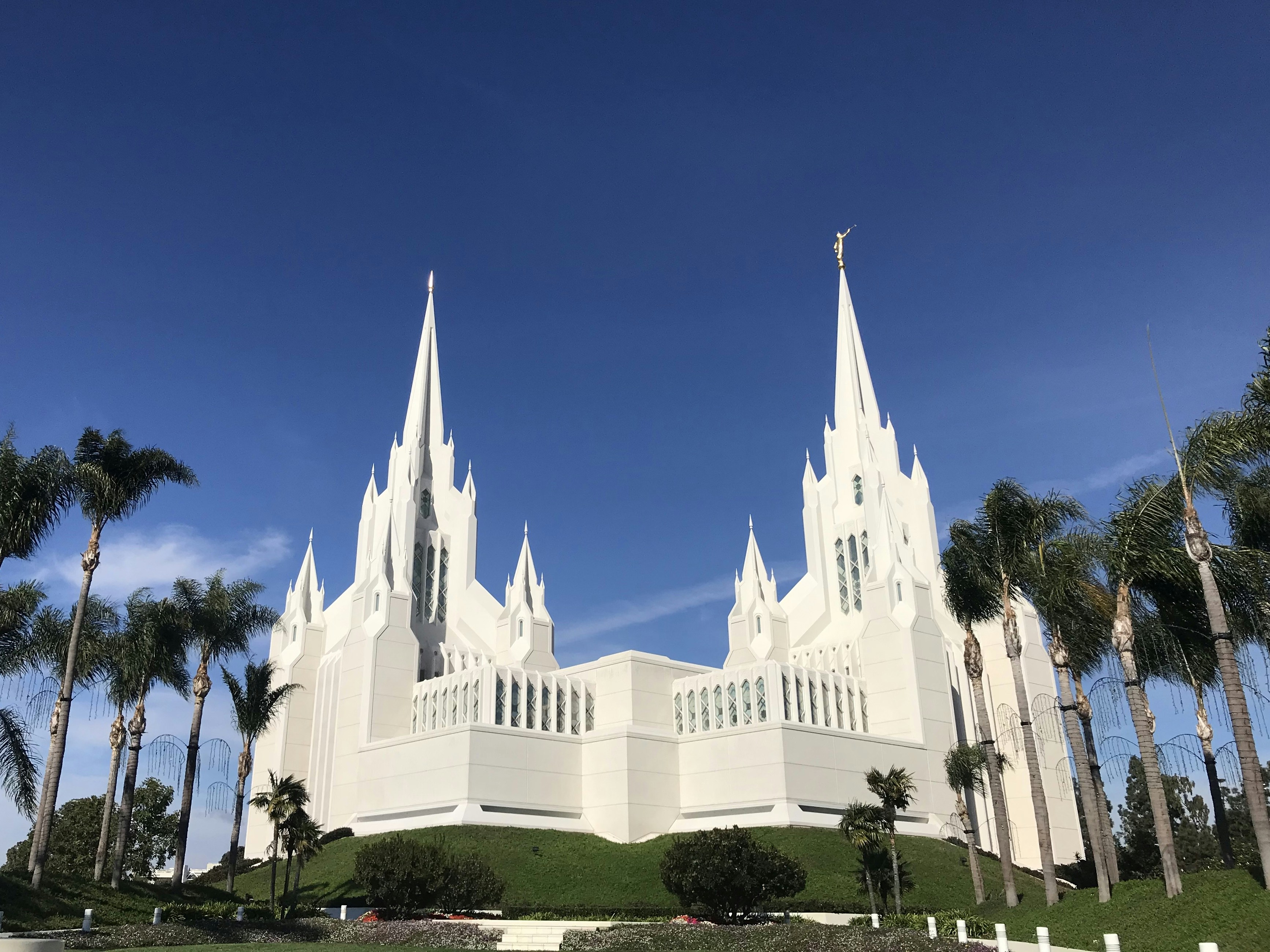 Majestic white church with towering spires surrounded by palm trees under a clear blue sky.