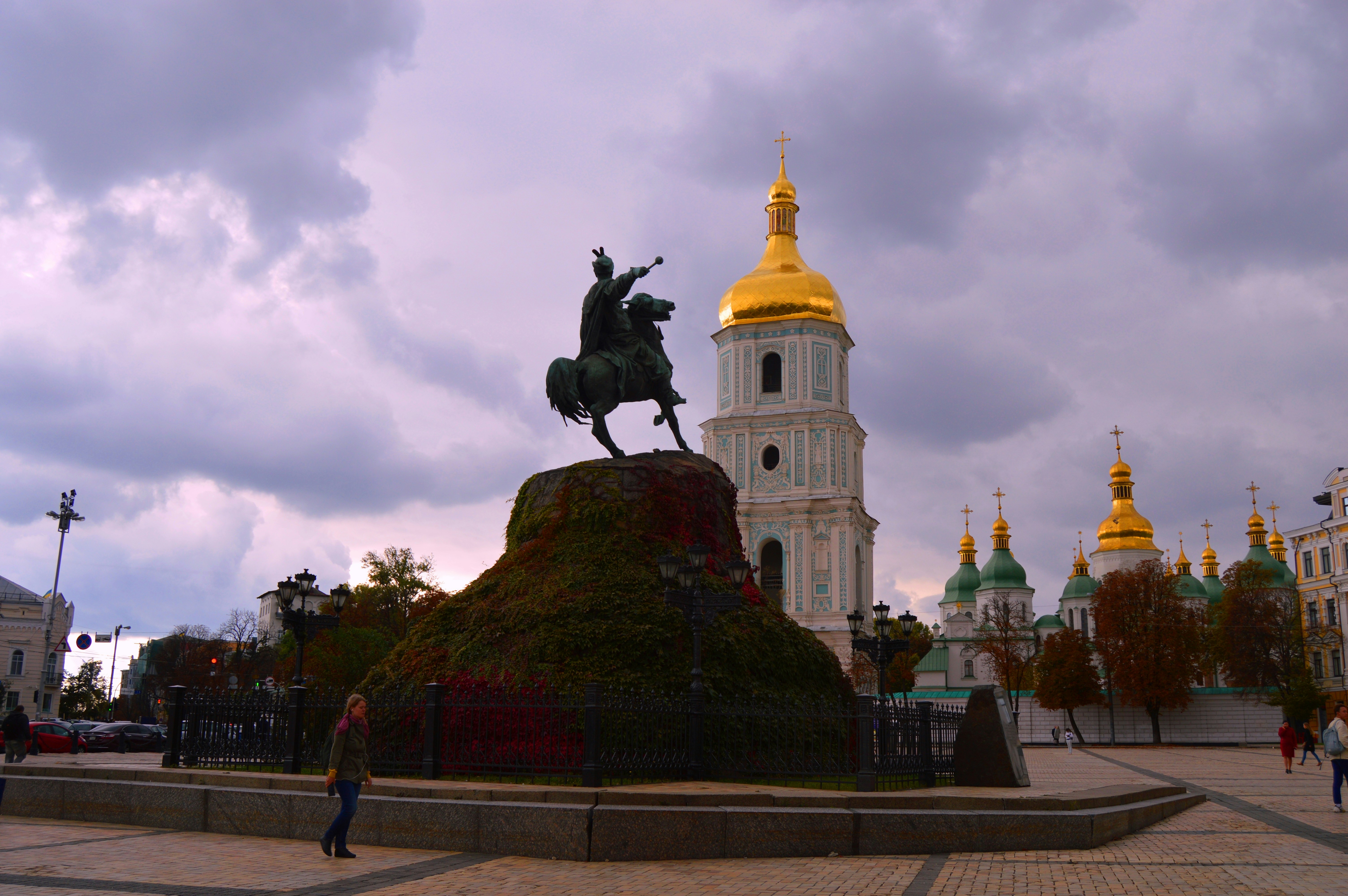 Equestrian statue silhouetted against dramatic clouds with golden-domed cathedral in the background.