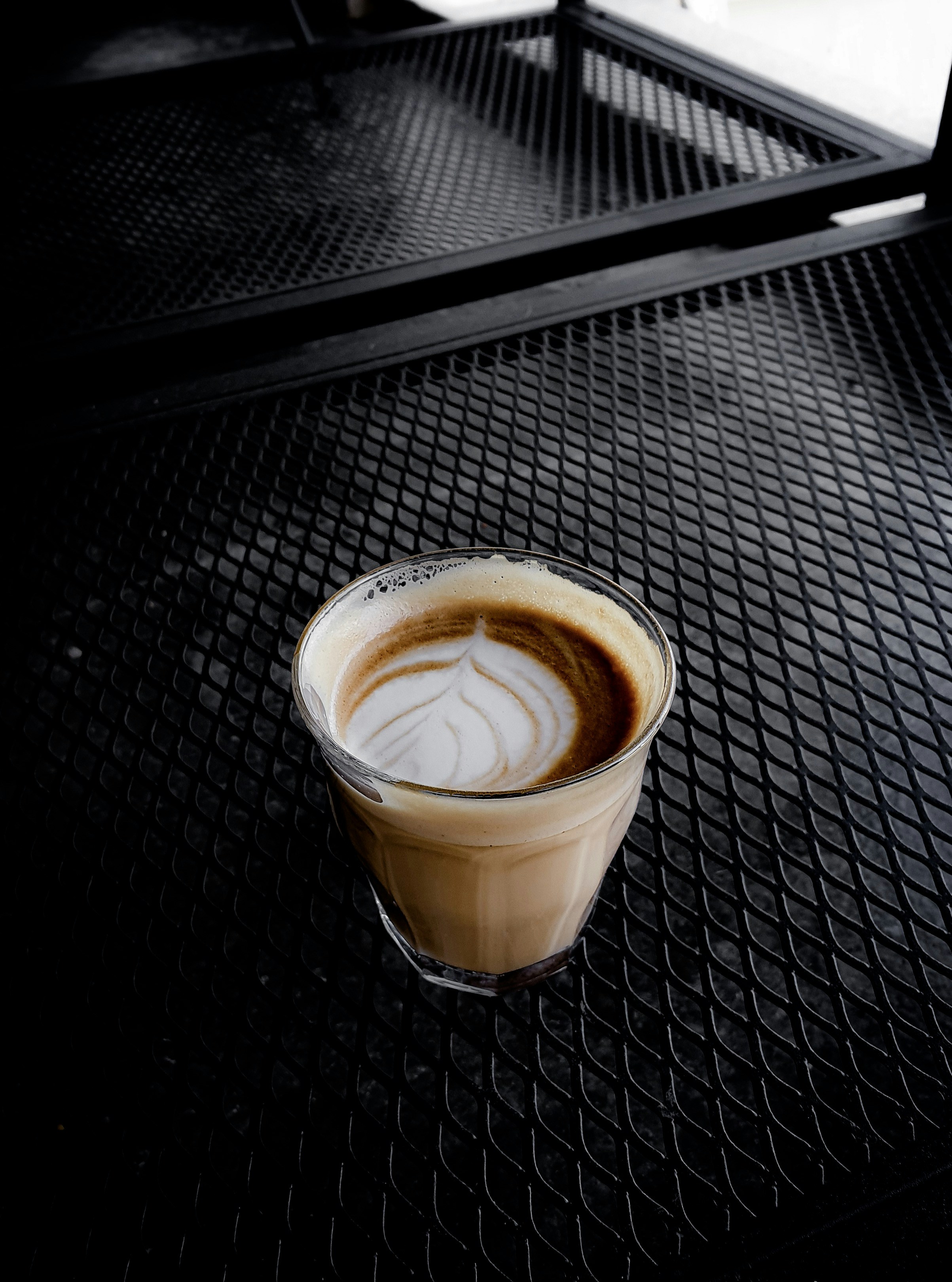 Coffee cup with intricate latte art resting on a textured black surface.