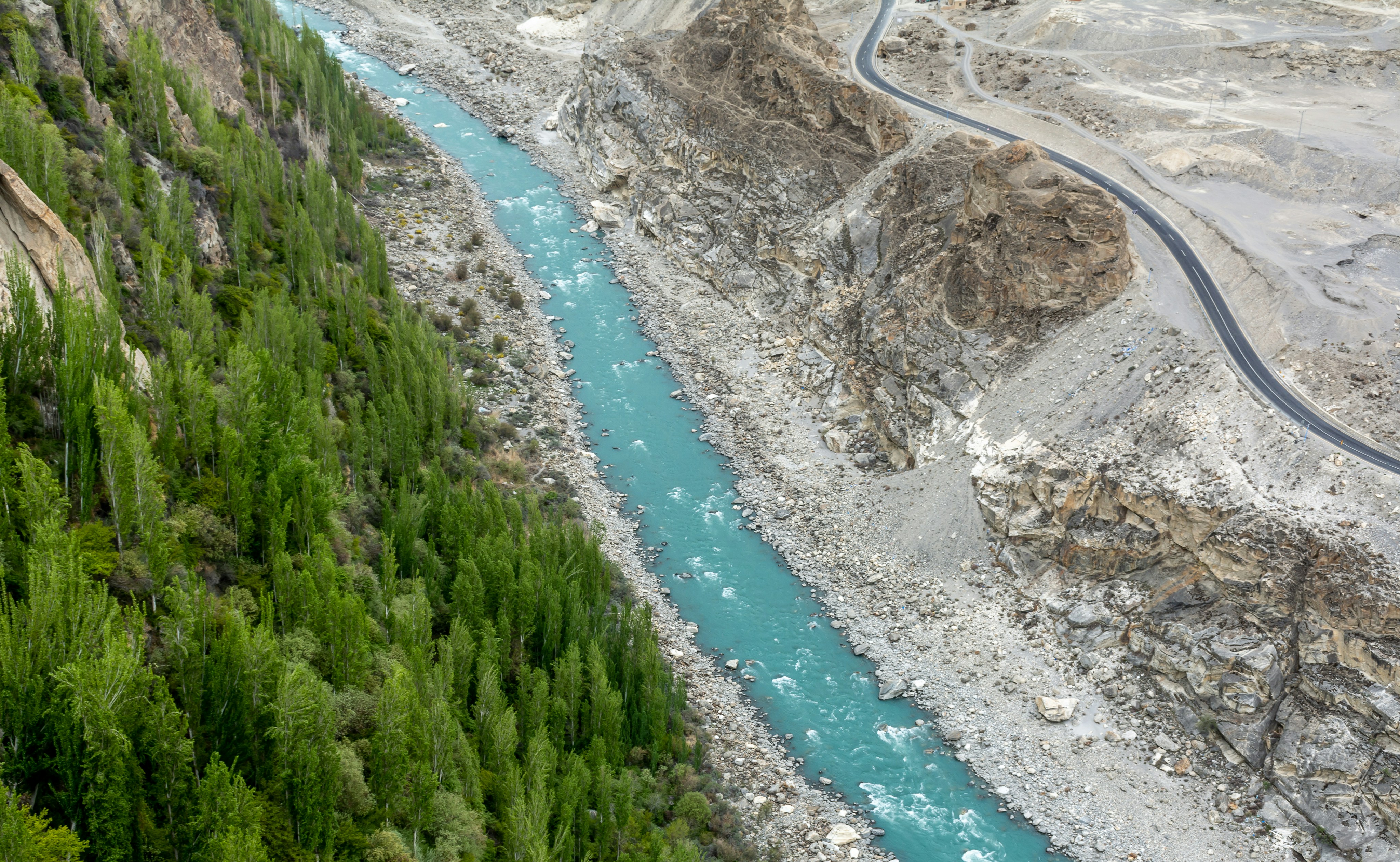 Turquoise river flows between lush green forest and rocky landscape.