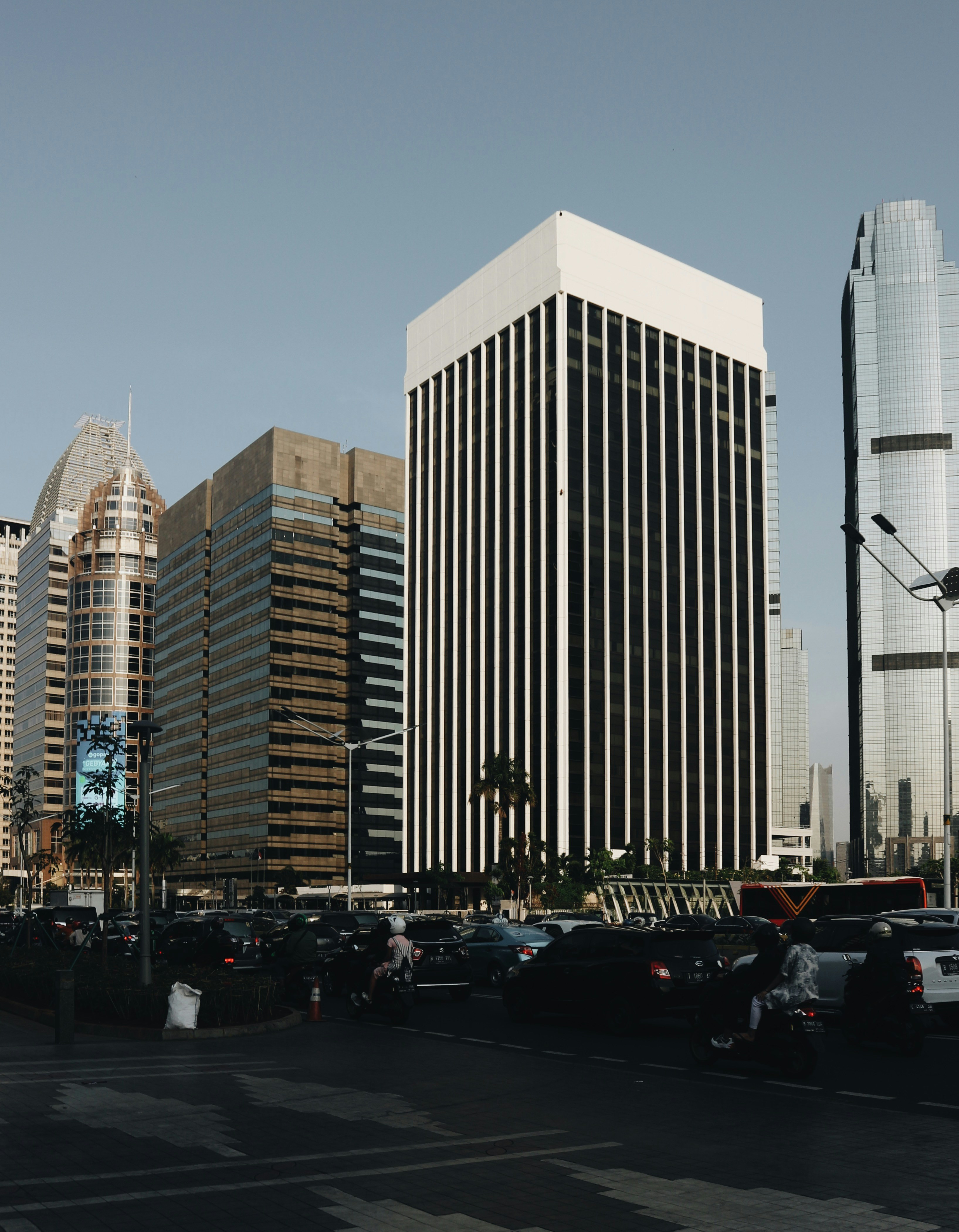 City street scene with a row of high-rise buildings under a clear blue sky and heavy traffic along the curb.