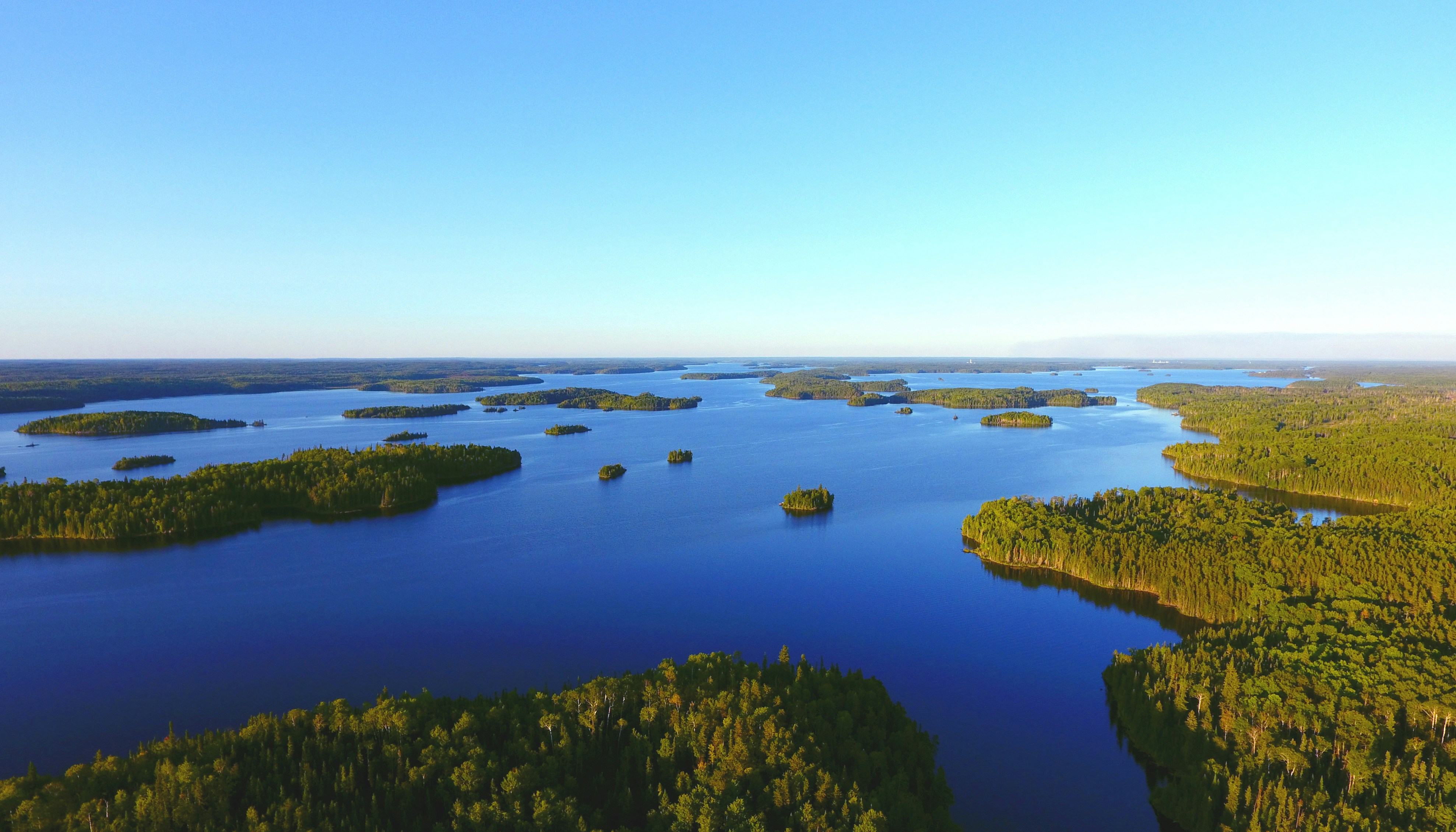 Aerial view of a sprawling lake dotted with lush green islands under a clear blue sky.