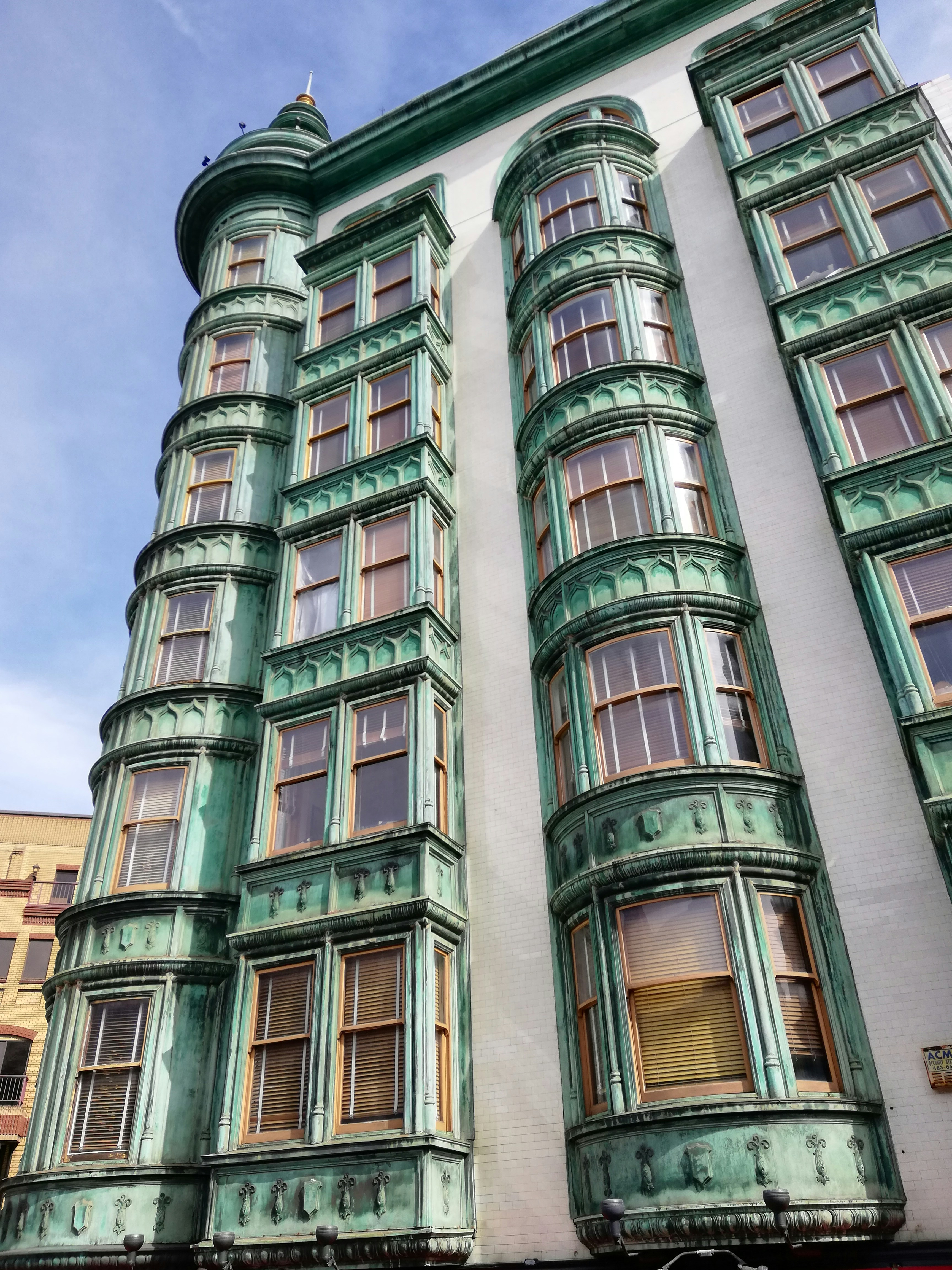 A green, turreted building façade with rounded bay windows stacks against a pale sky. The architectural detail and vertical rhythm define the composition.